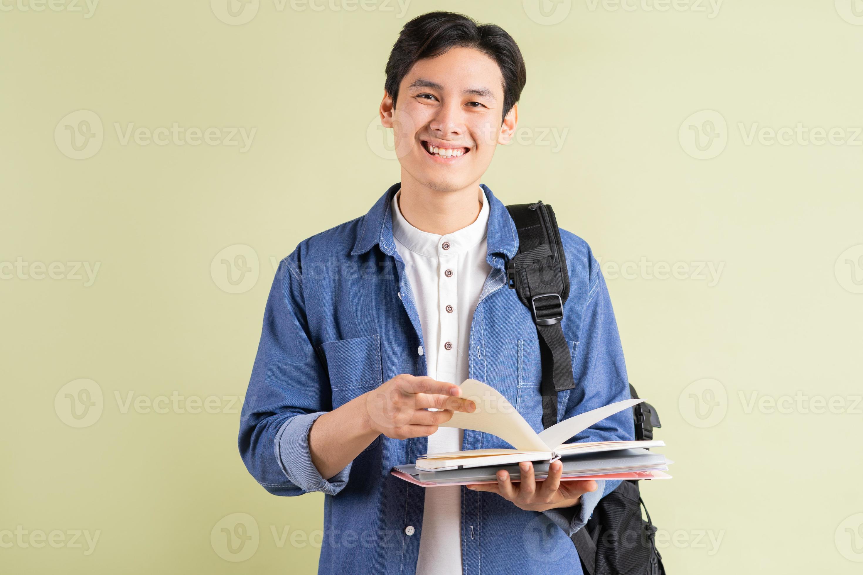 Photo of handsome Asian student smiling and holding book in hand ...