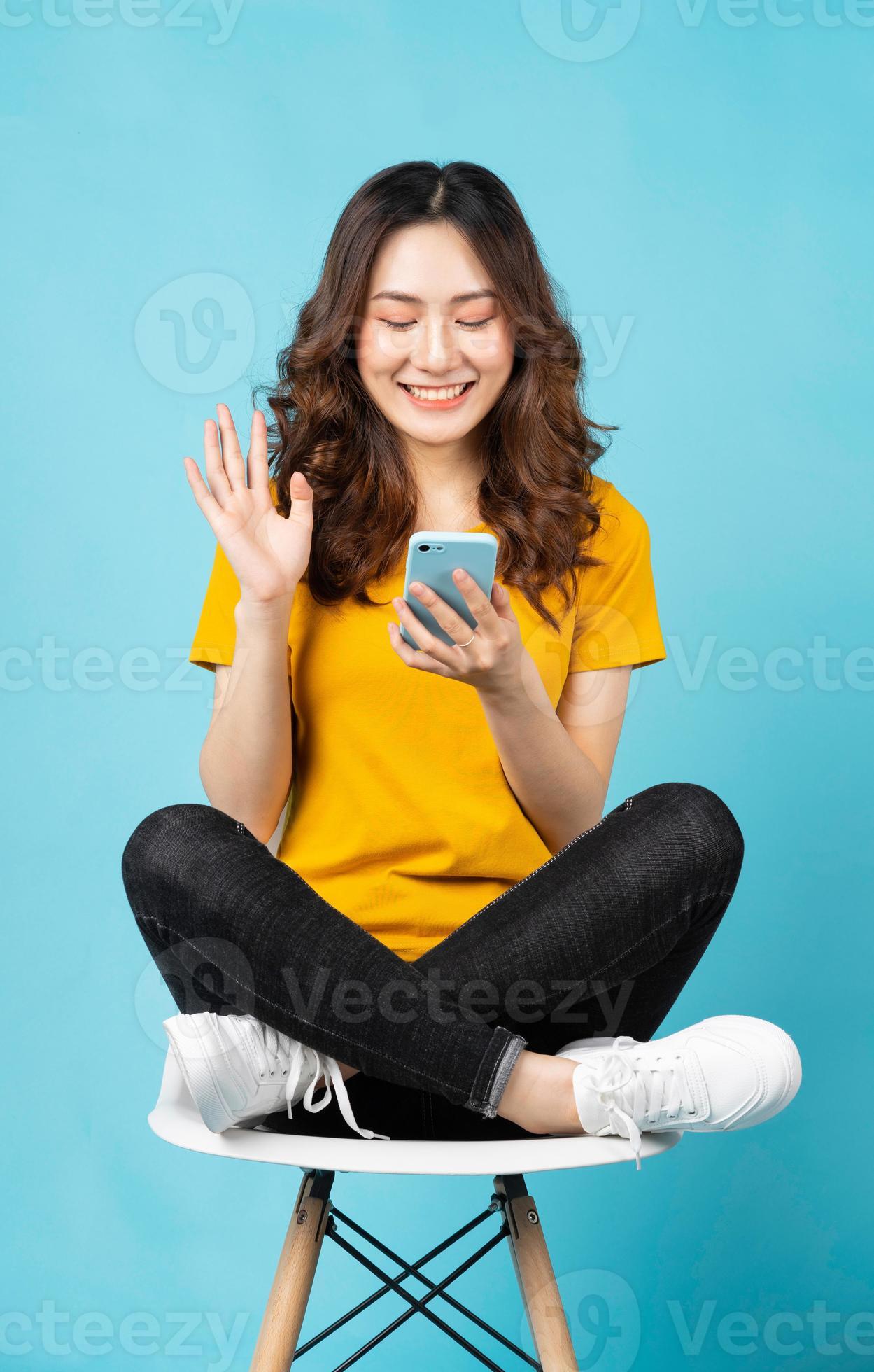 Young Asian Girl Sitting In Chair Using Phone With Cheerful Expression