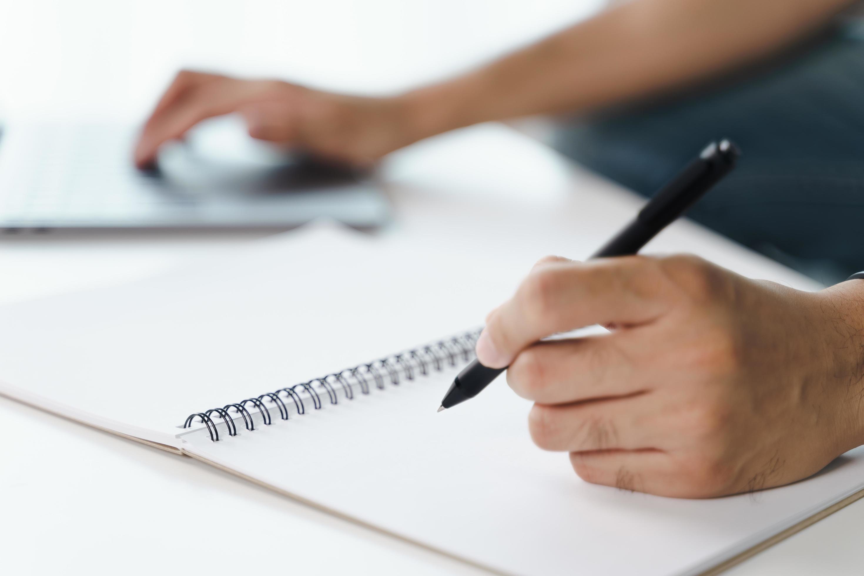 Young man hands writing down on the notepad, notebook and use laptop ...
