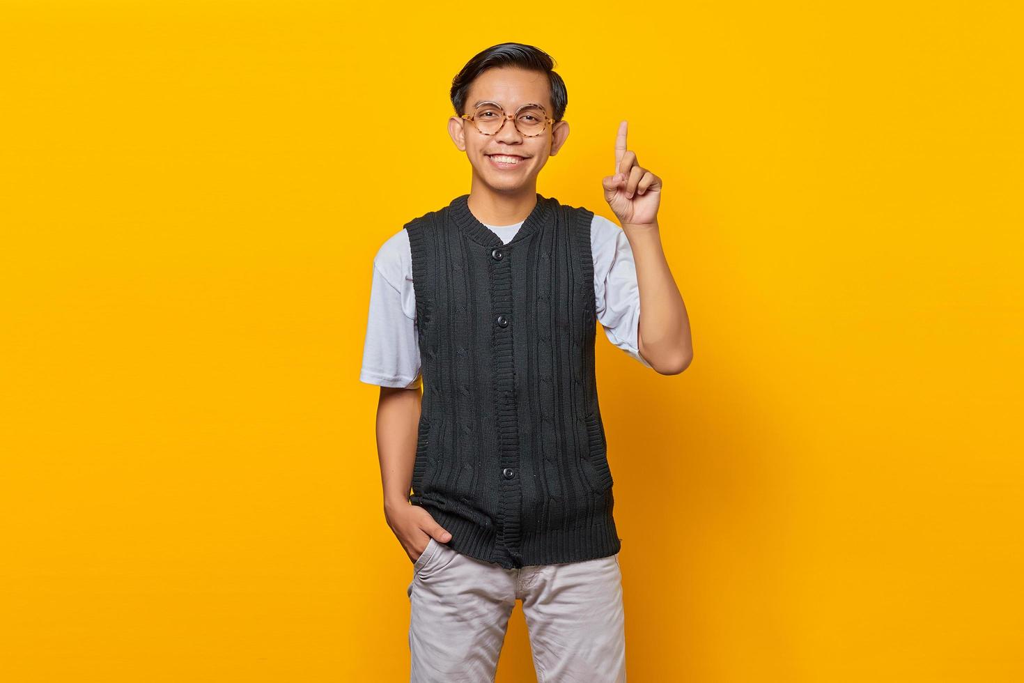 Cheerful asian young man pointing up to copy space isolated over yellow ...