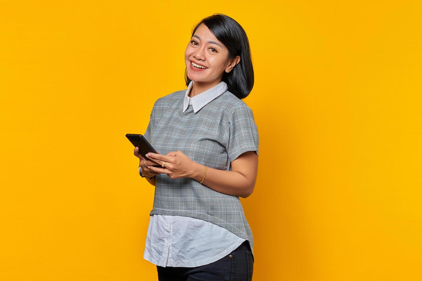 Portrait Of Smiling Young Asian Woman Holding Mobile Phone On Yellow