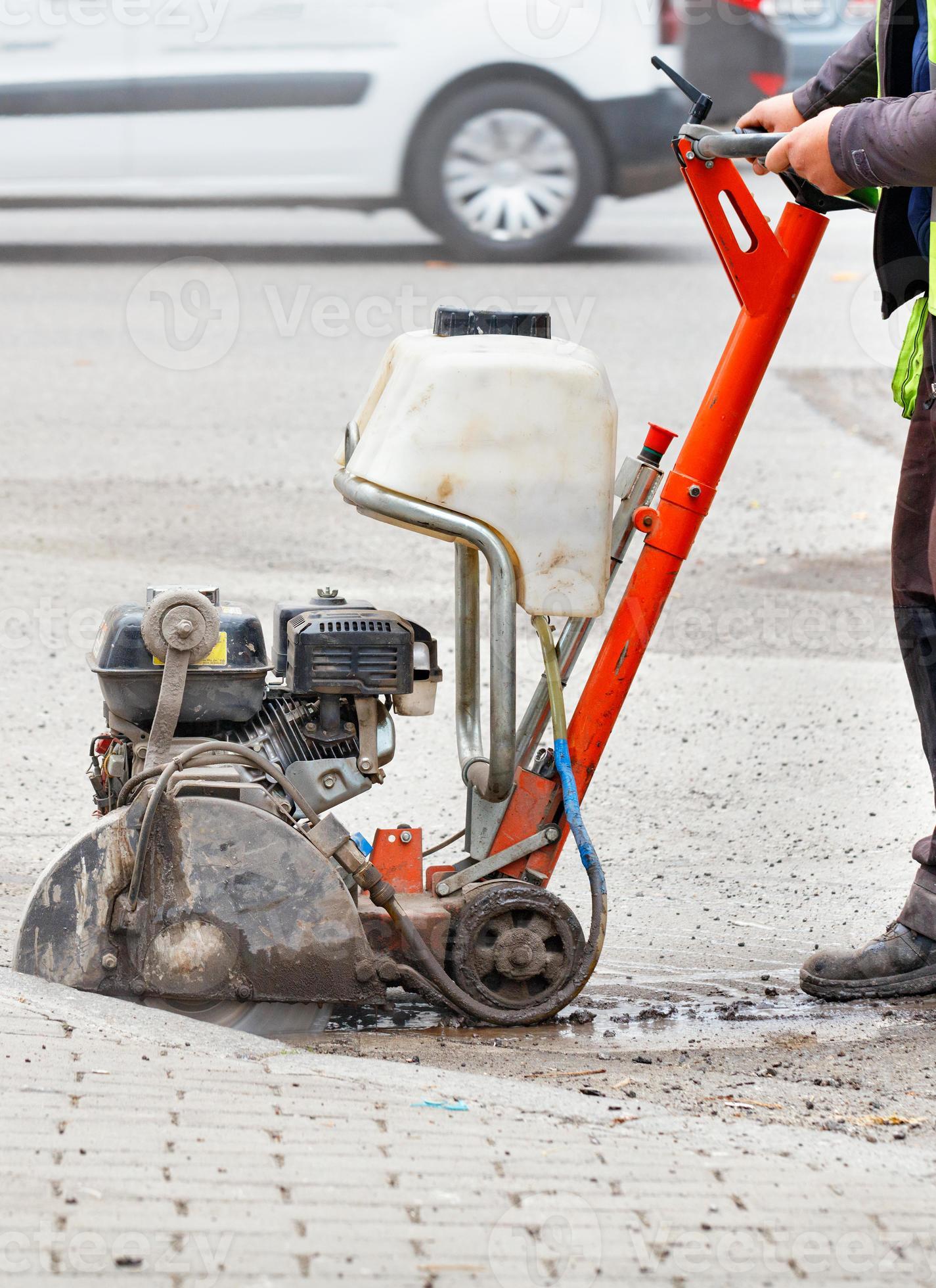 A worker cuts old asphalt with a petrol cutter on the roadway against ...