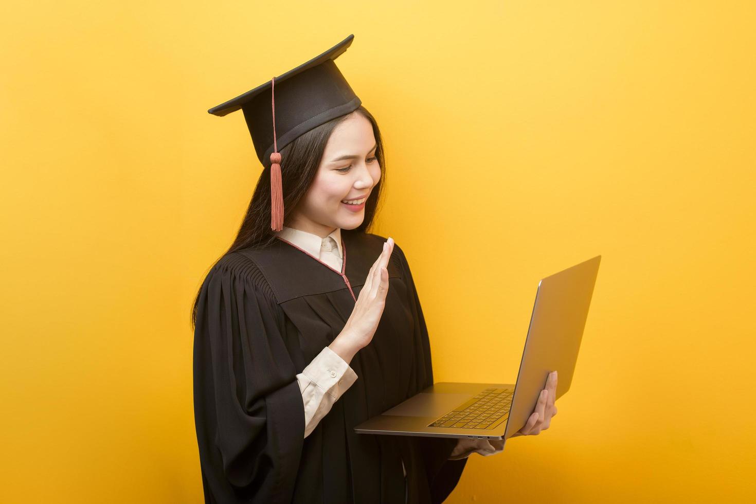 portrait of beautiful woman in graduation gown is holding laptop ...