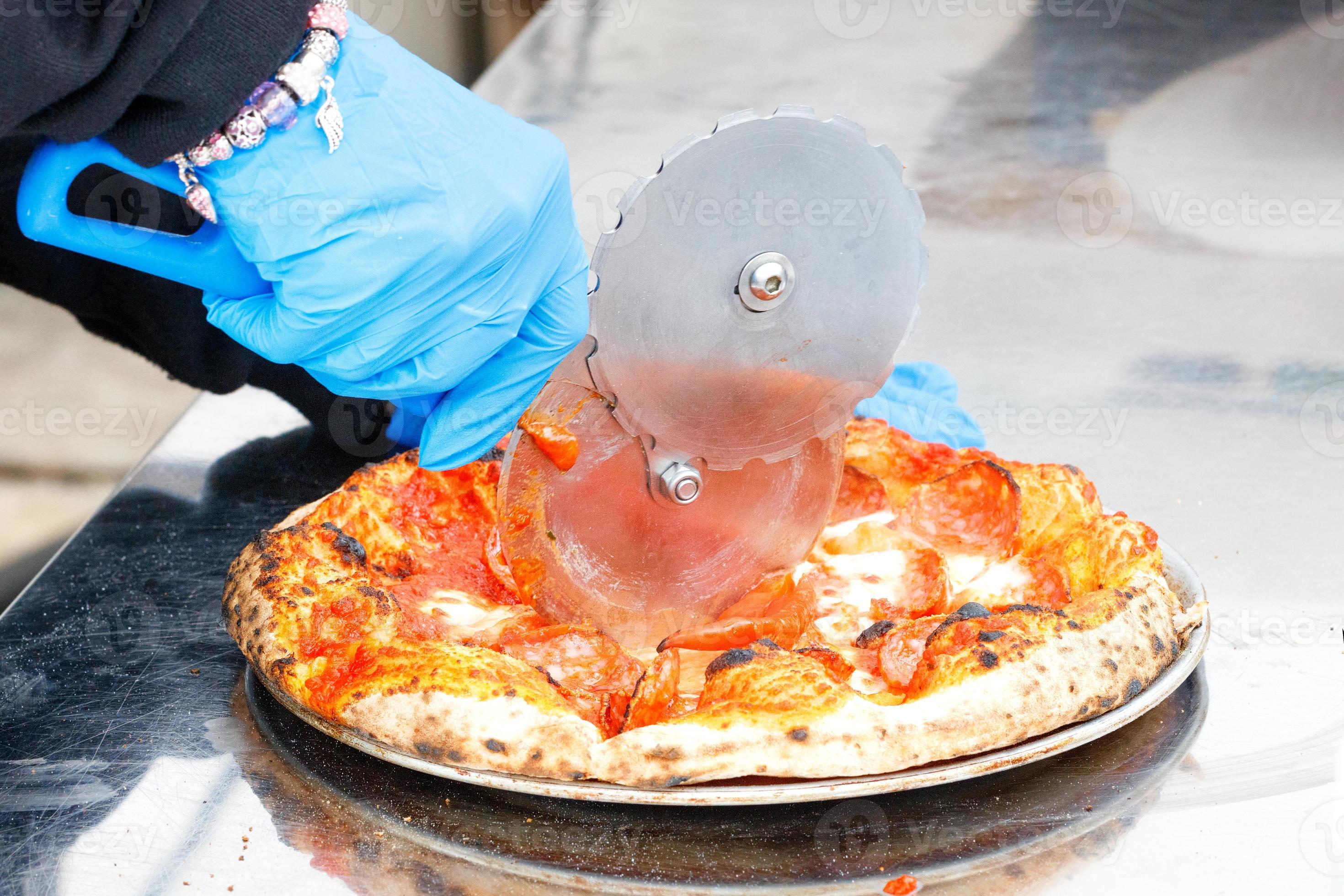 A Man Wearing Blue Latex Gloves Is Cutting A Cooked Pizza With A Round a-man-wearing-blue-latex-gloves-is-cutting-a-cooked-pizza-with-a-round
