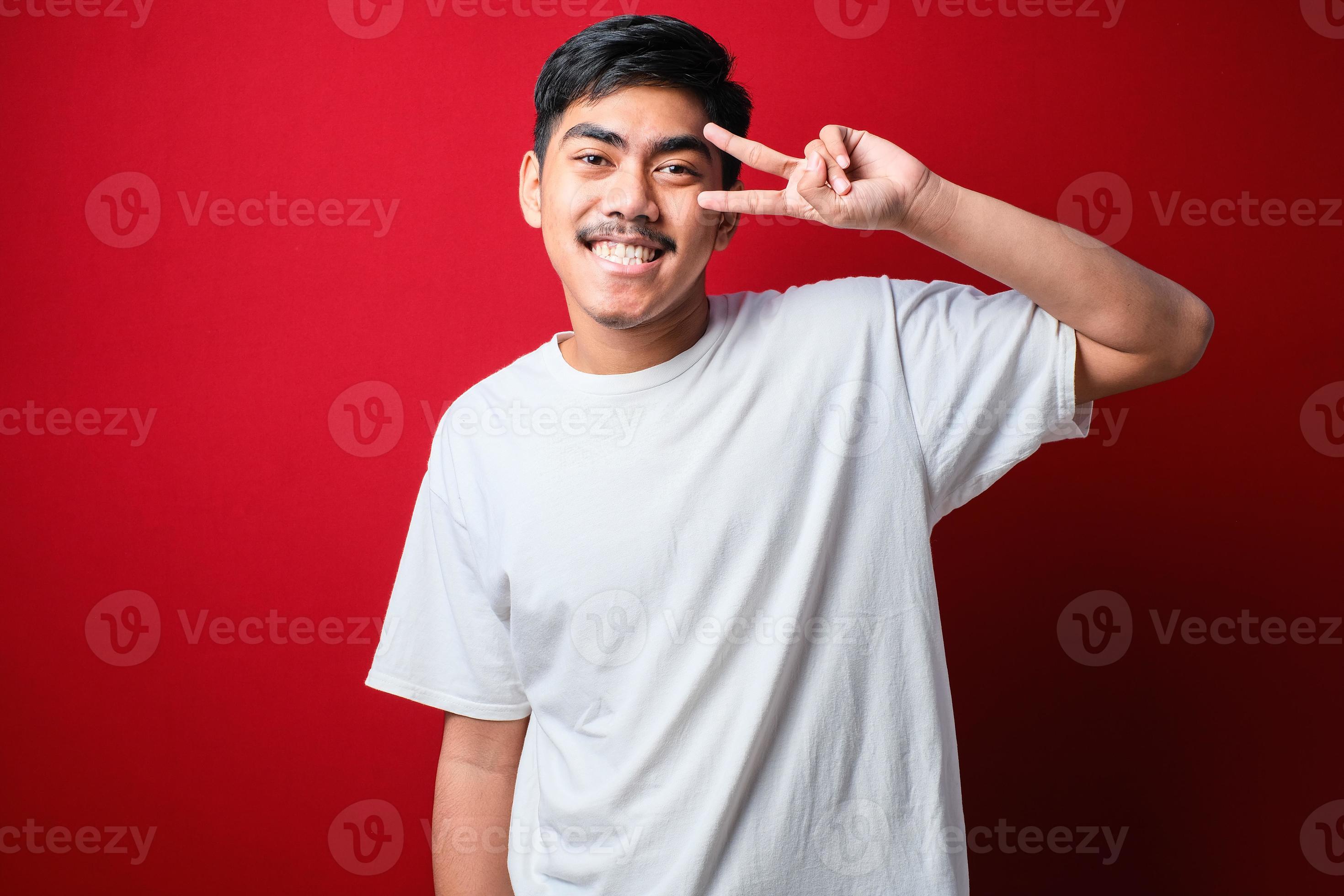 Young handsome asian guy wearing white t-shirt doing peace symbol with ...