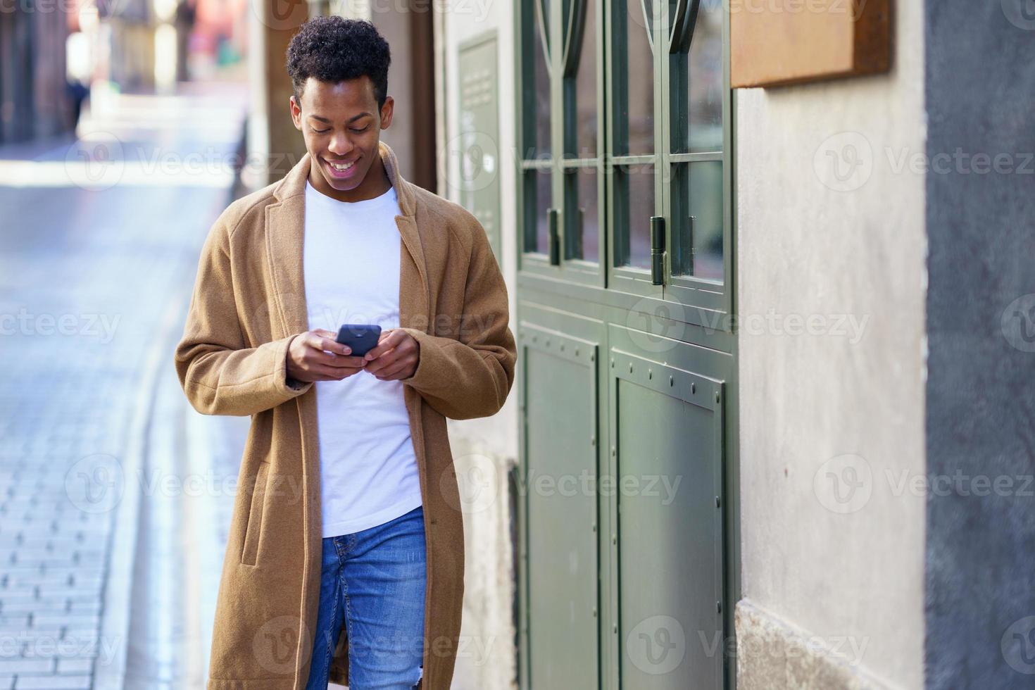 Young Black Man Consulting His Phone While Walking Down The Street