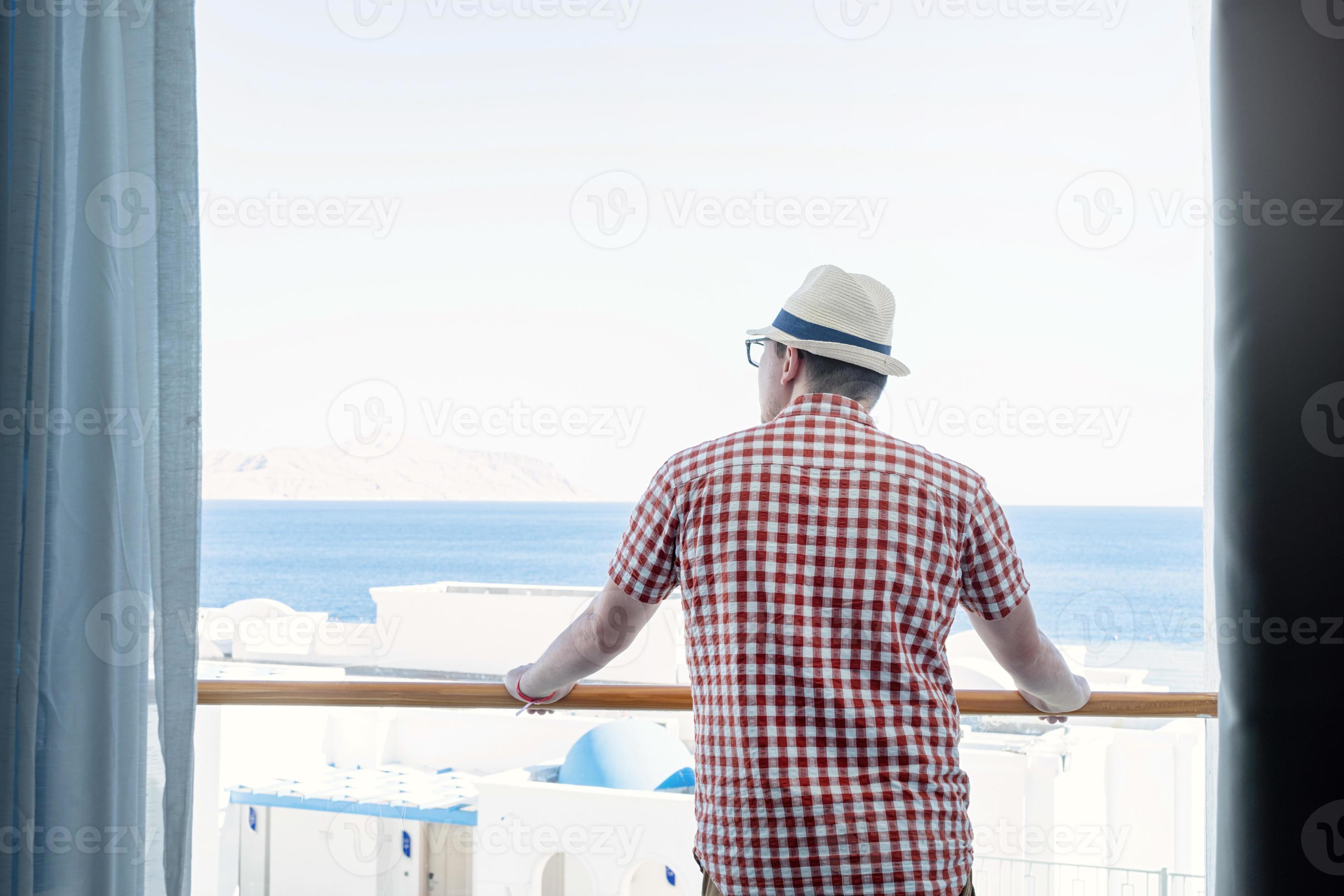 Handsome Caucasian young man standing on balcony of hotel, looking at ...