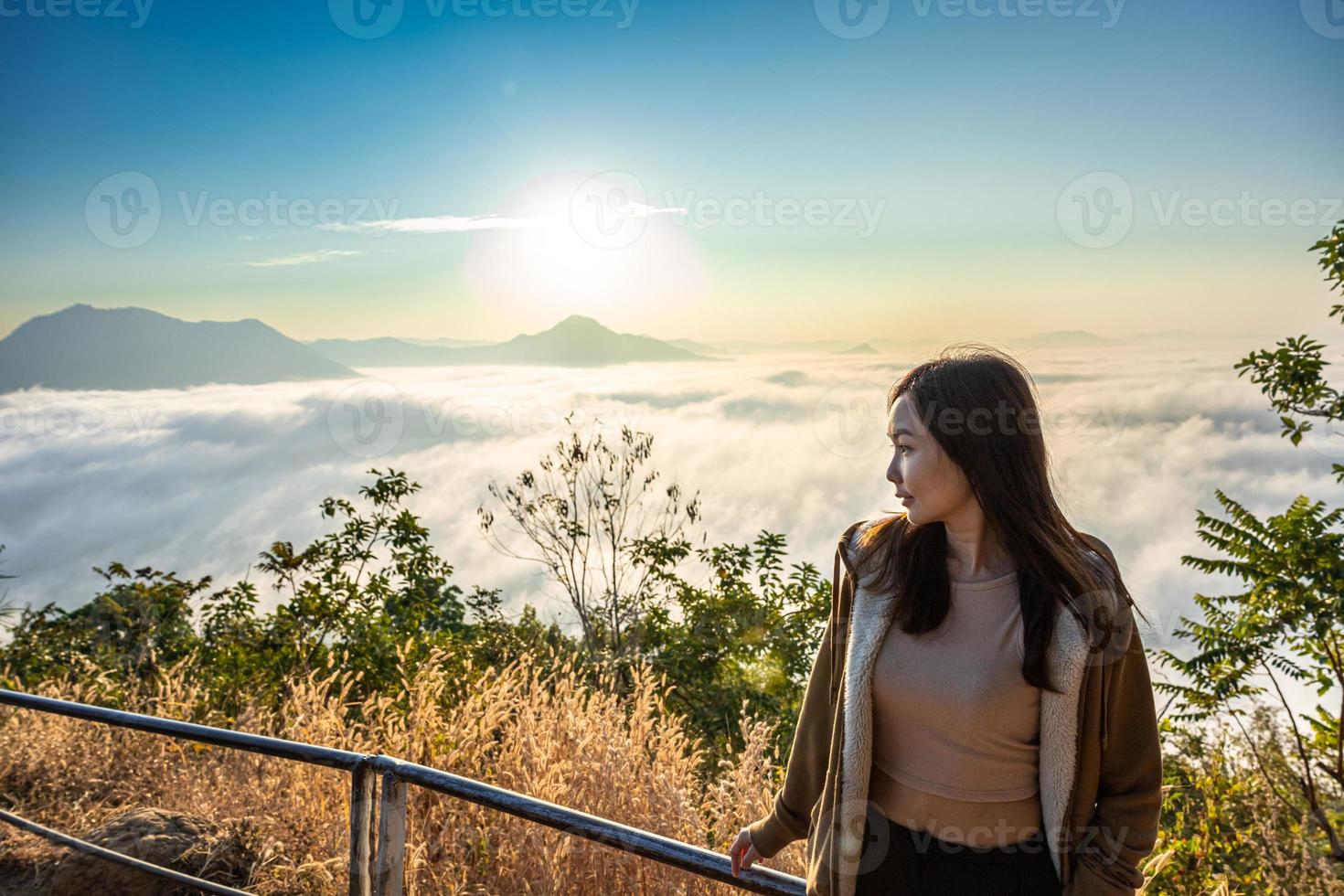 Asian woman with background of Sea of Fog covers and golden sunrise the area on the top of hill ...