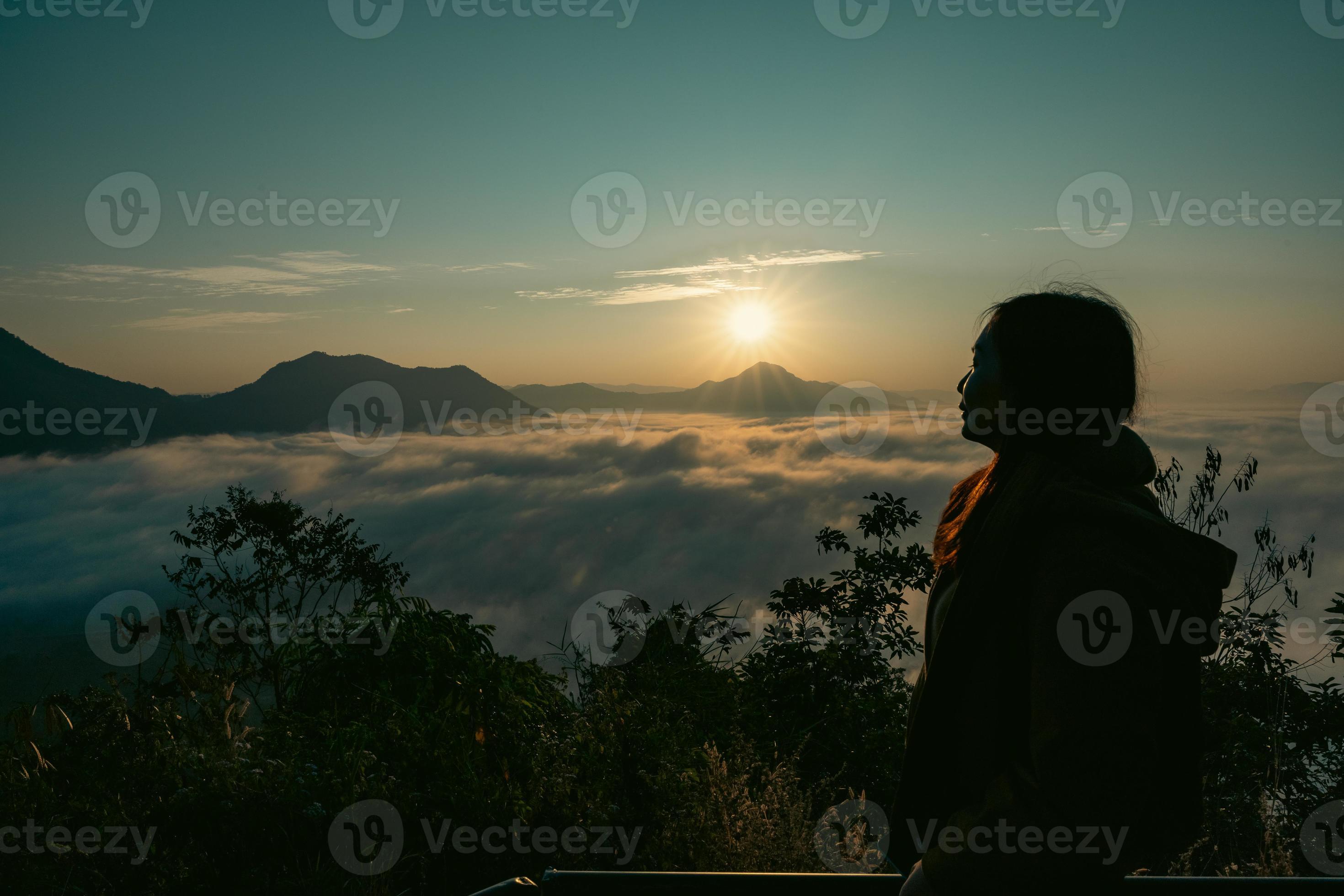 Asian woman with background of Sea of Fog covers and golden sunrise the area on the top of hill ...