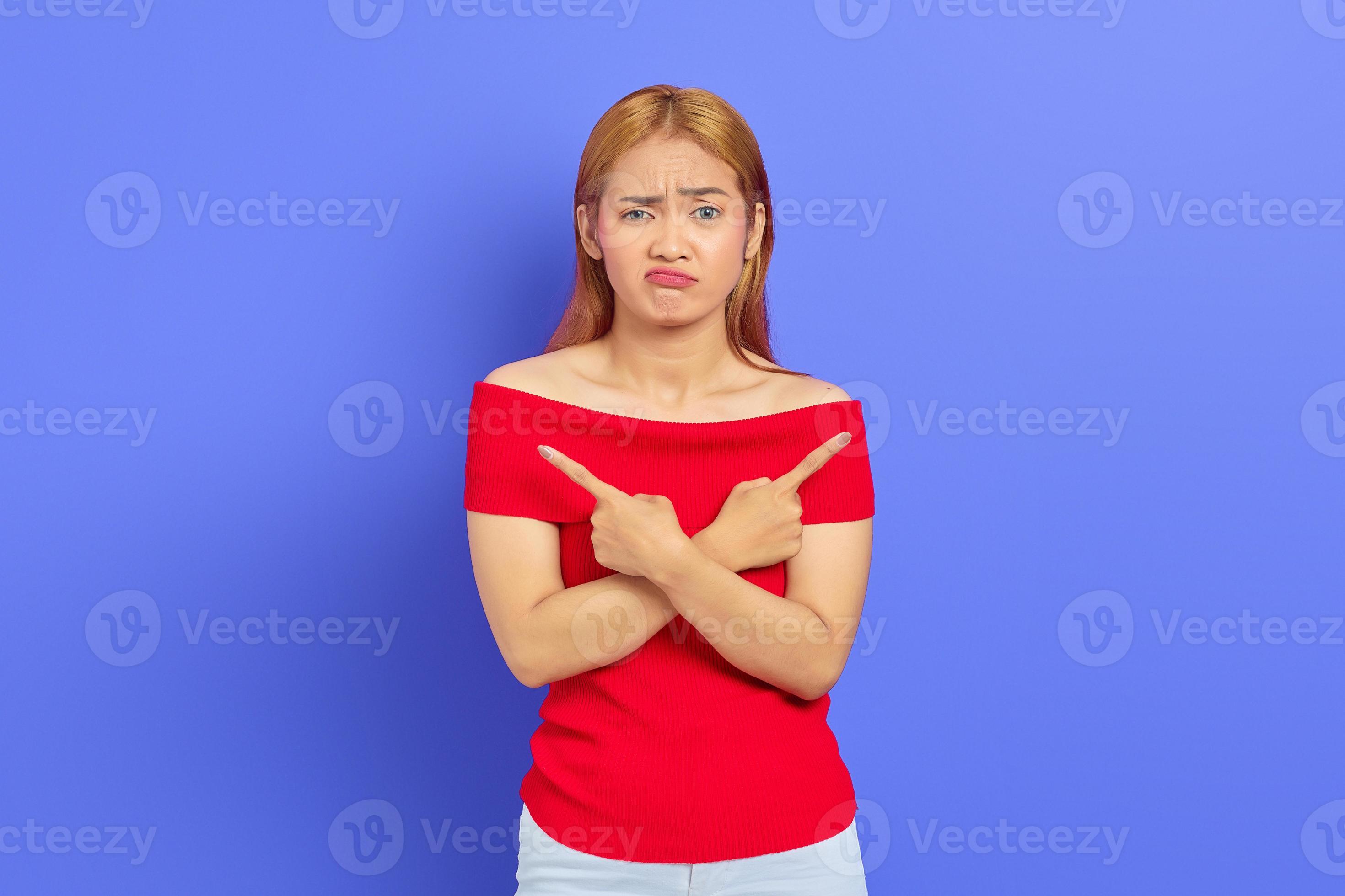 Portrait of confused young Asian woman standing and pointing to copy ...