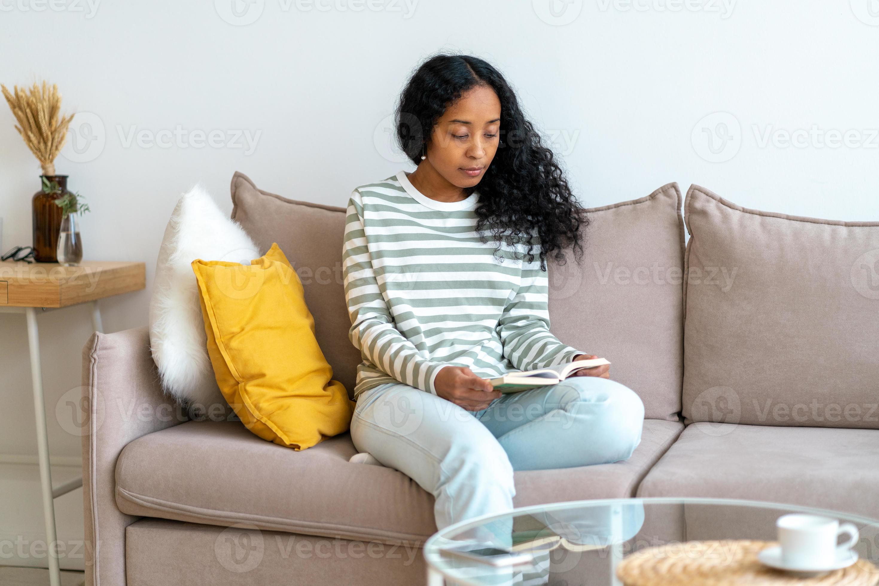 African American Female Reading Book While Sitting On Sofa In Cozy