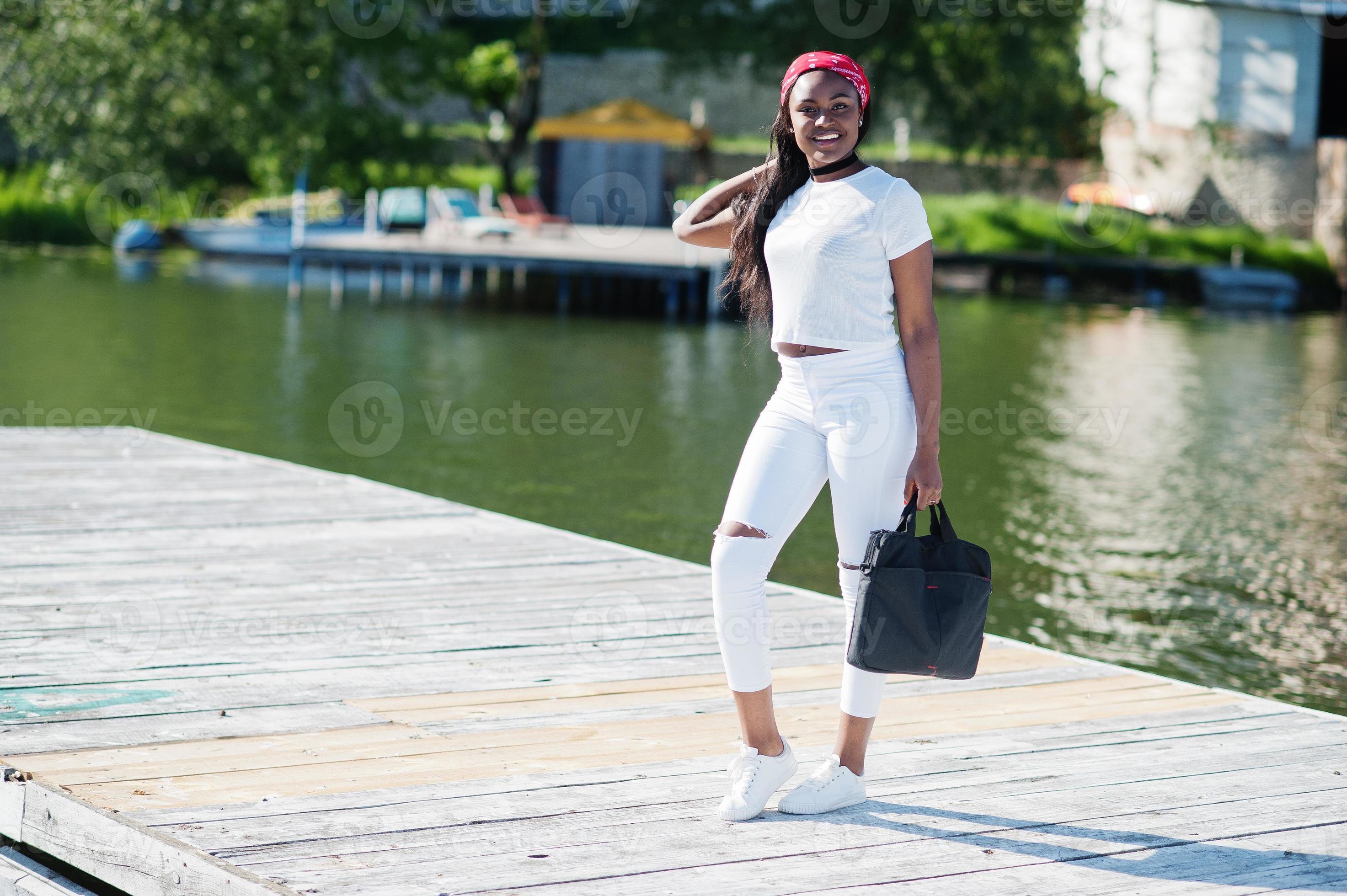 Portrait Of Stylish African American Girl Wear On White Clothes With Bag On Hand Against Pier 0337