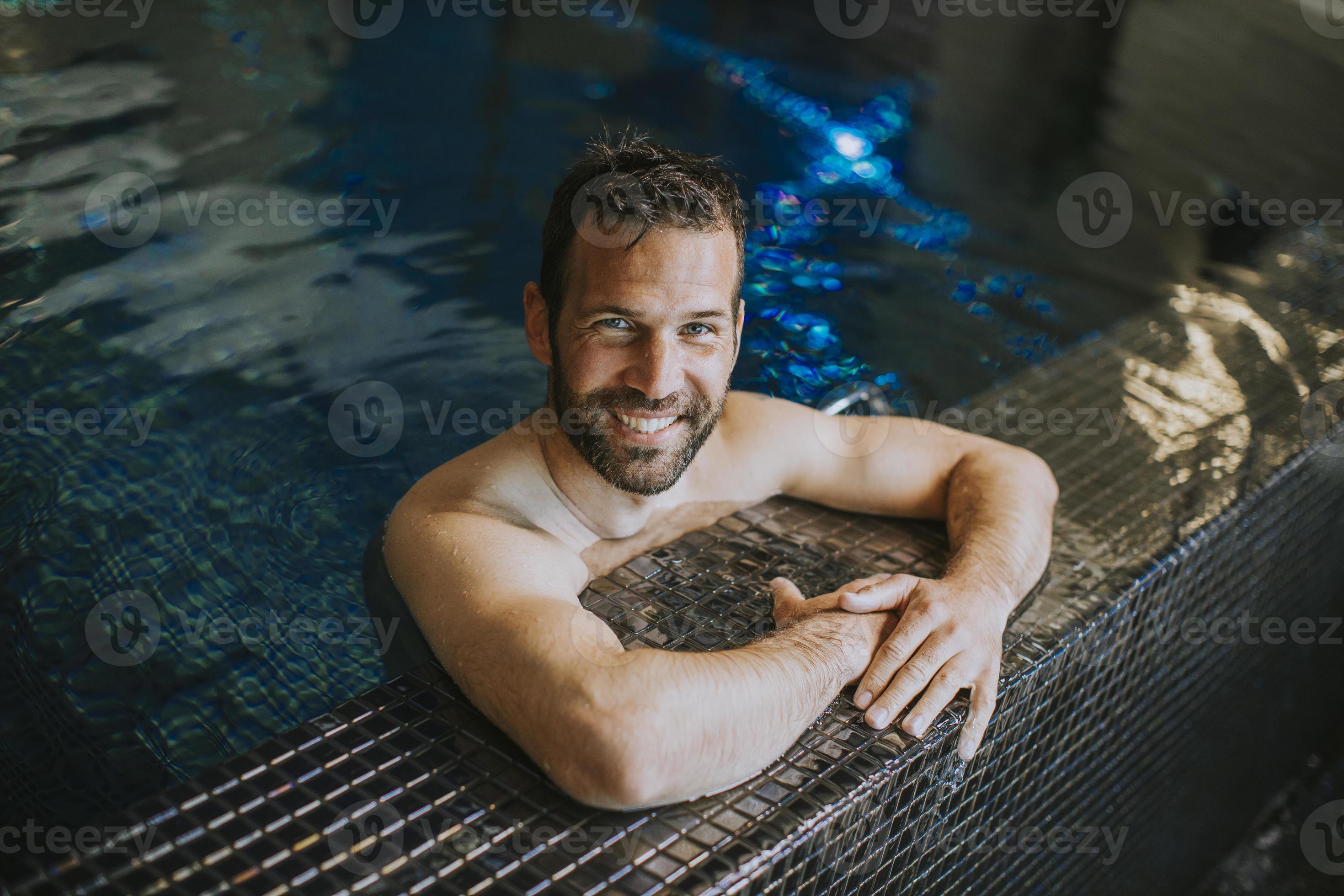 Portrait of smiling young man relaxing by the swimming pool edge ...