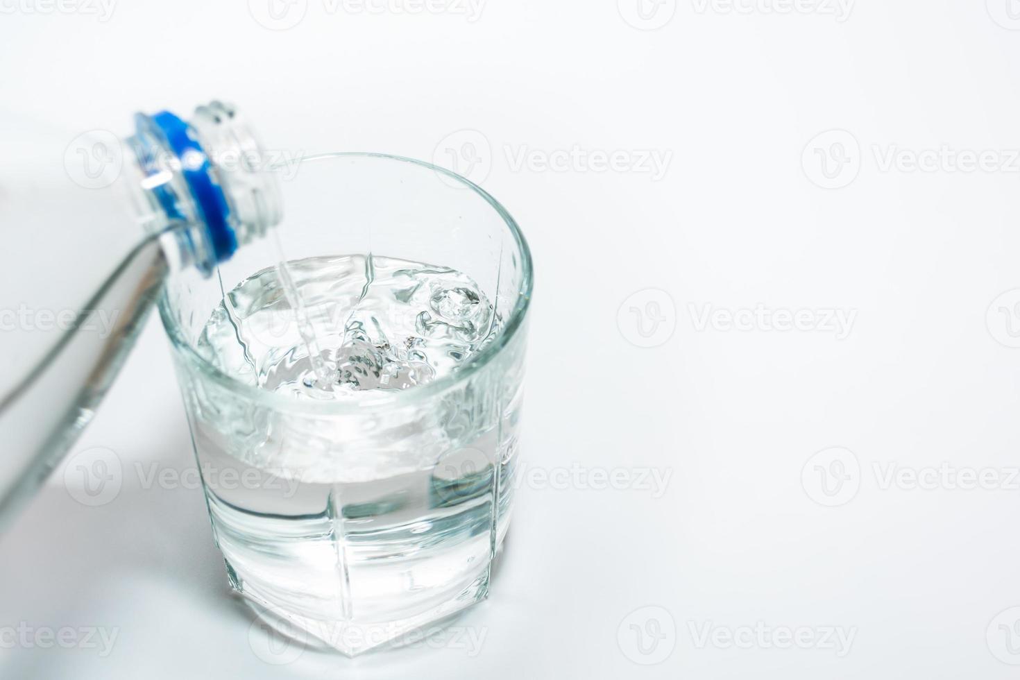 Pouring pure fresh mineral non-carbonated water into a glass beaker on a white background from a ...