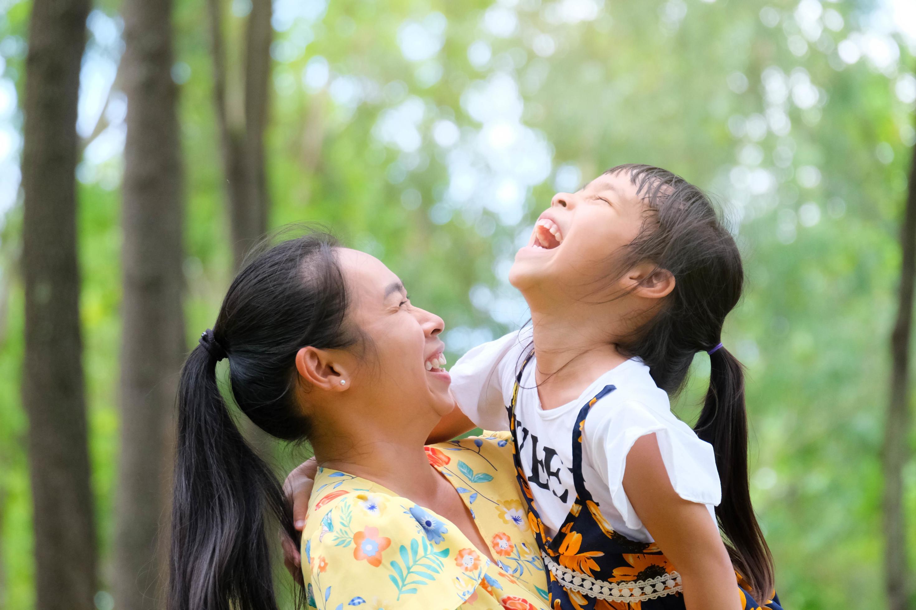 Young mother hugging with her daughter in the park. Smiling little girl playing with mother in ...