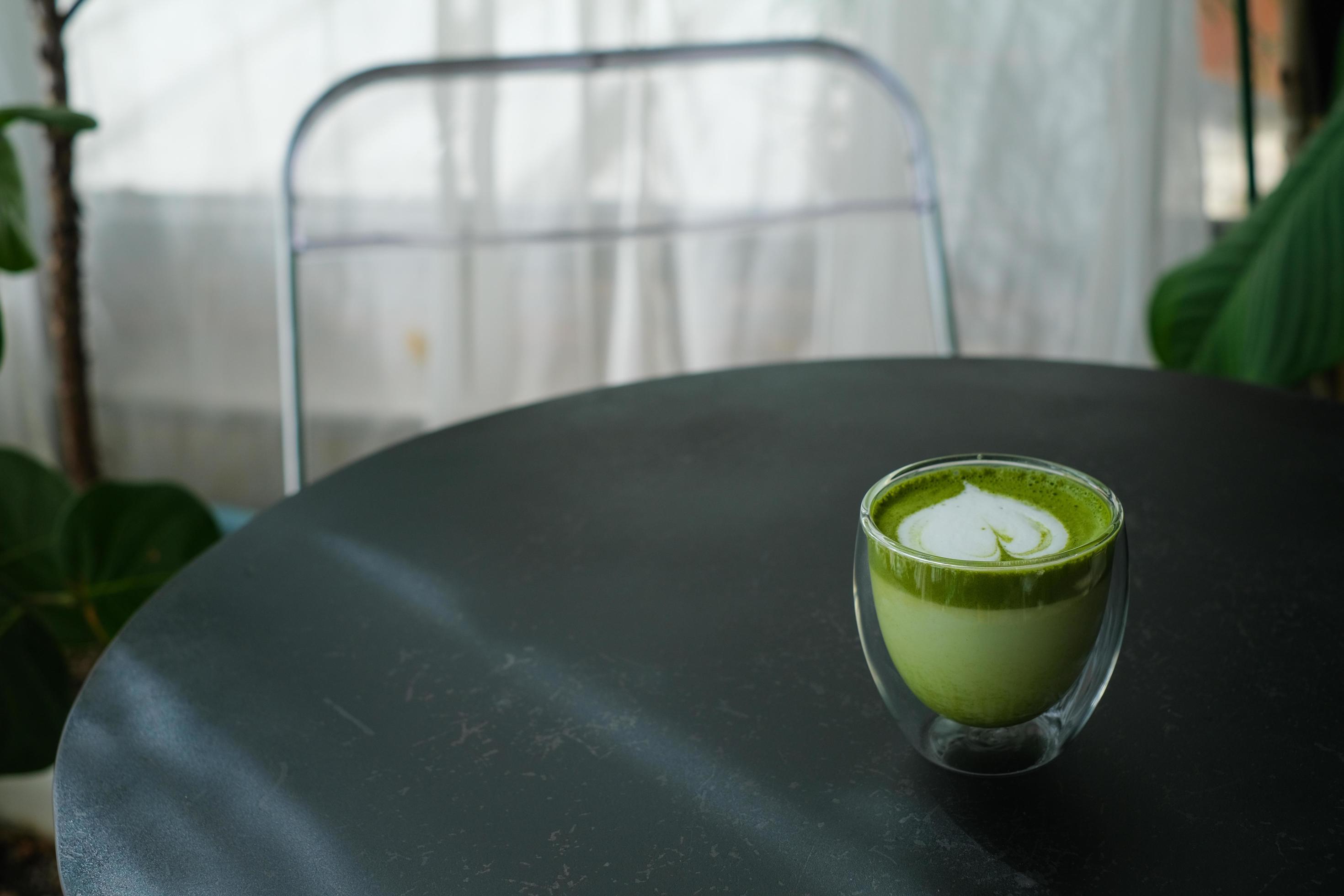 Colse up hot matcha green tea latte art in double walled glass on table in the cafe. 8354400 ...