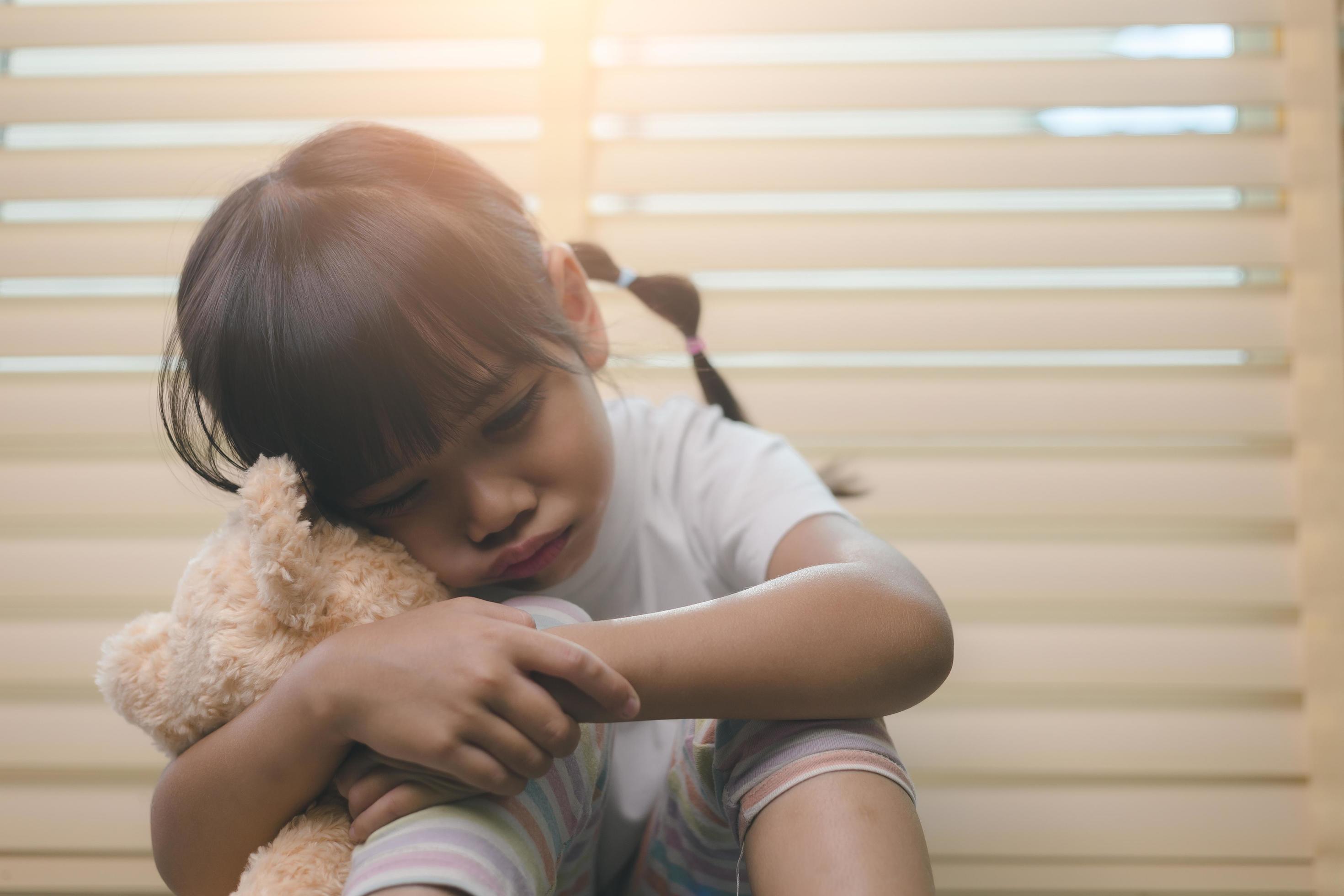 Close up lonely little girl hugging toy, sitting at home alone, upset ...