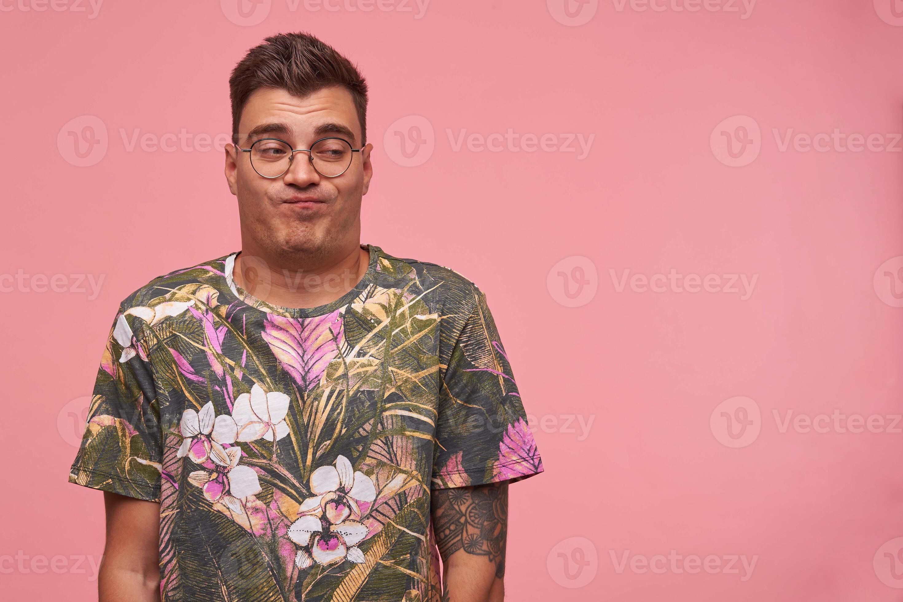 Funny pretty young male in flowered t-shirt and glasses looking aside ...