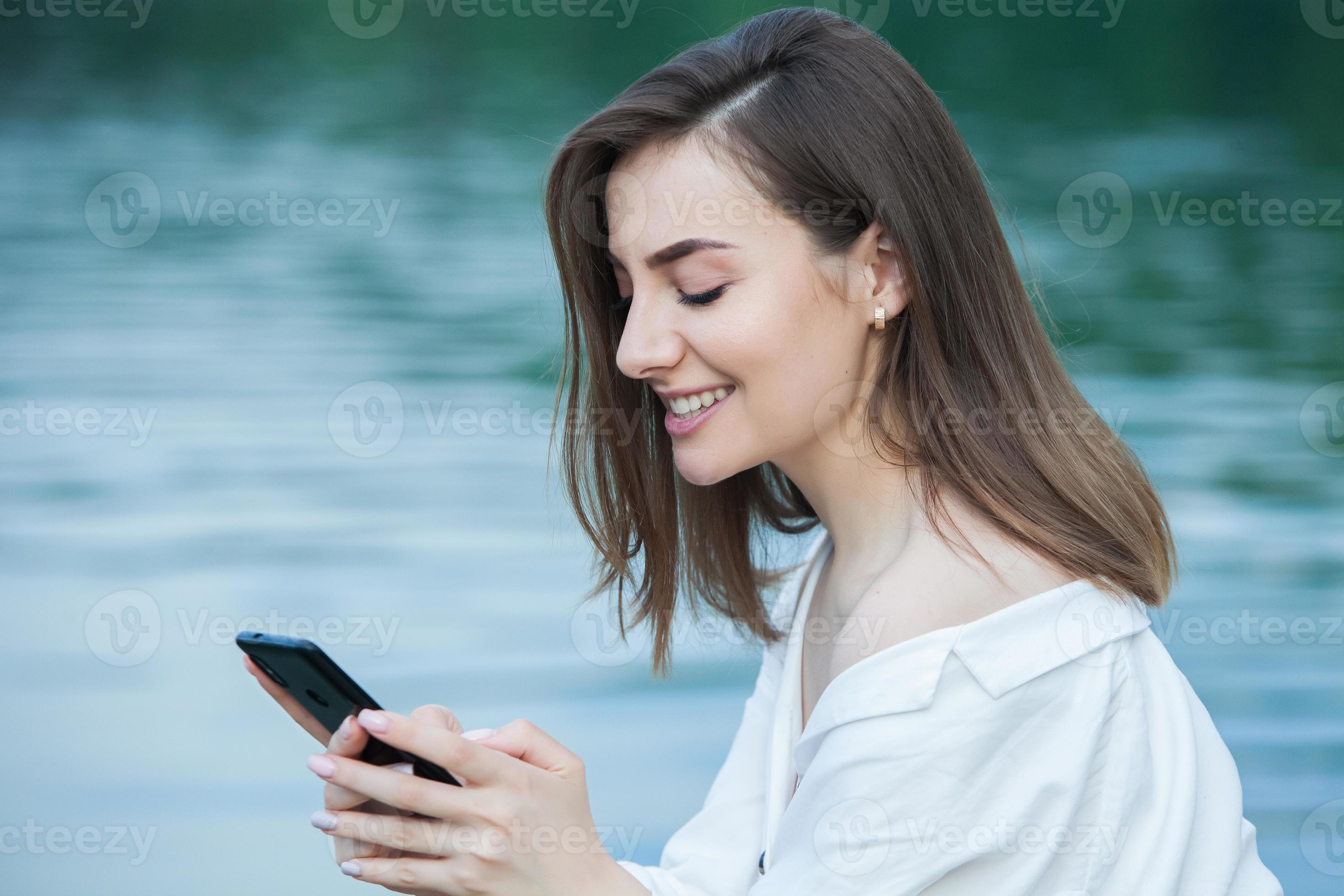 Girl outdoors texting on her mobile phone. Girl with phone. Portrait of a happy woman text sms ...