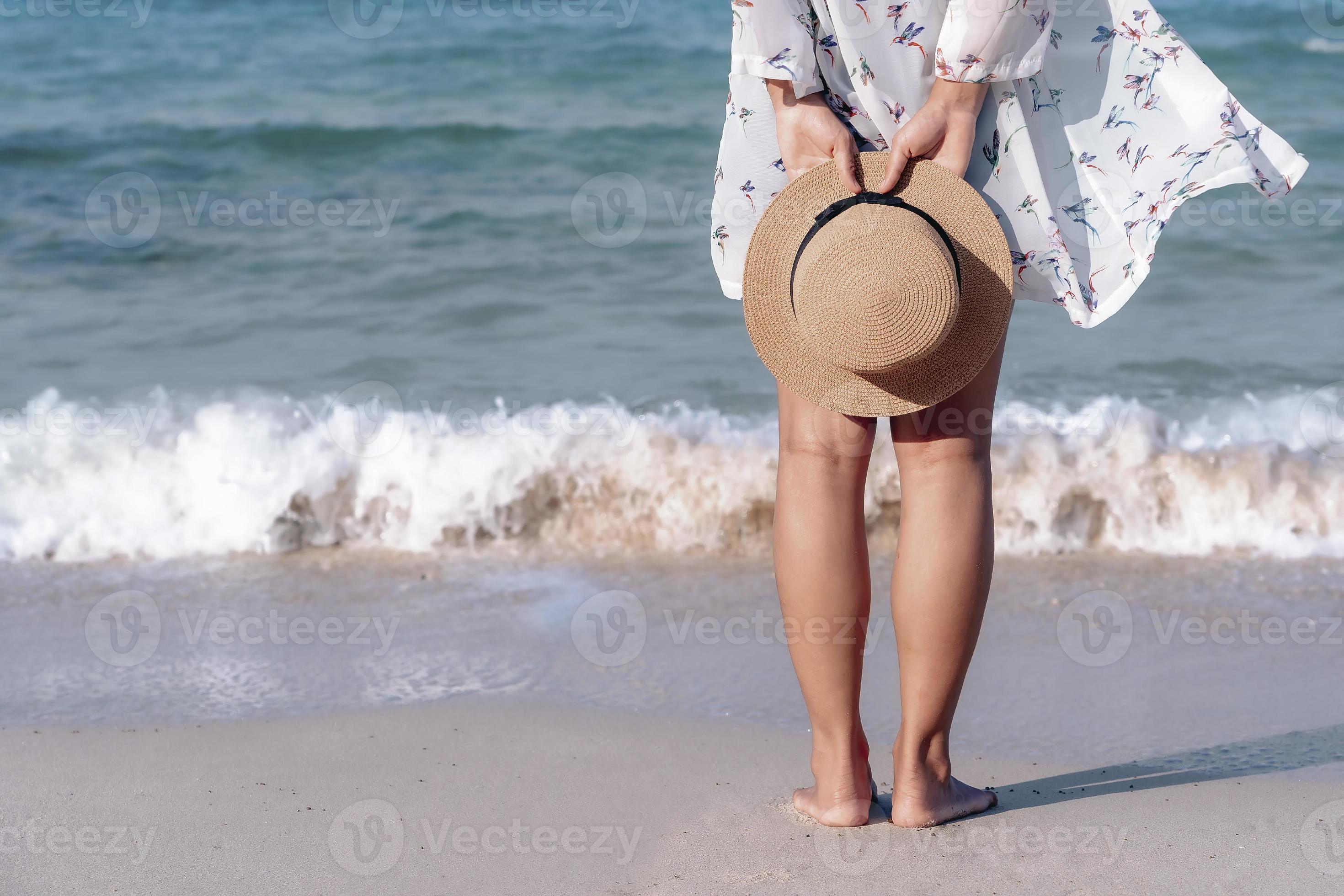 vista trasera de las piernas de una mujer parada en una playa de arena cerca del océano color ...
