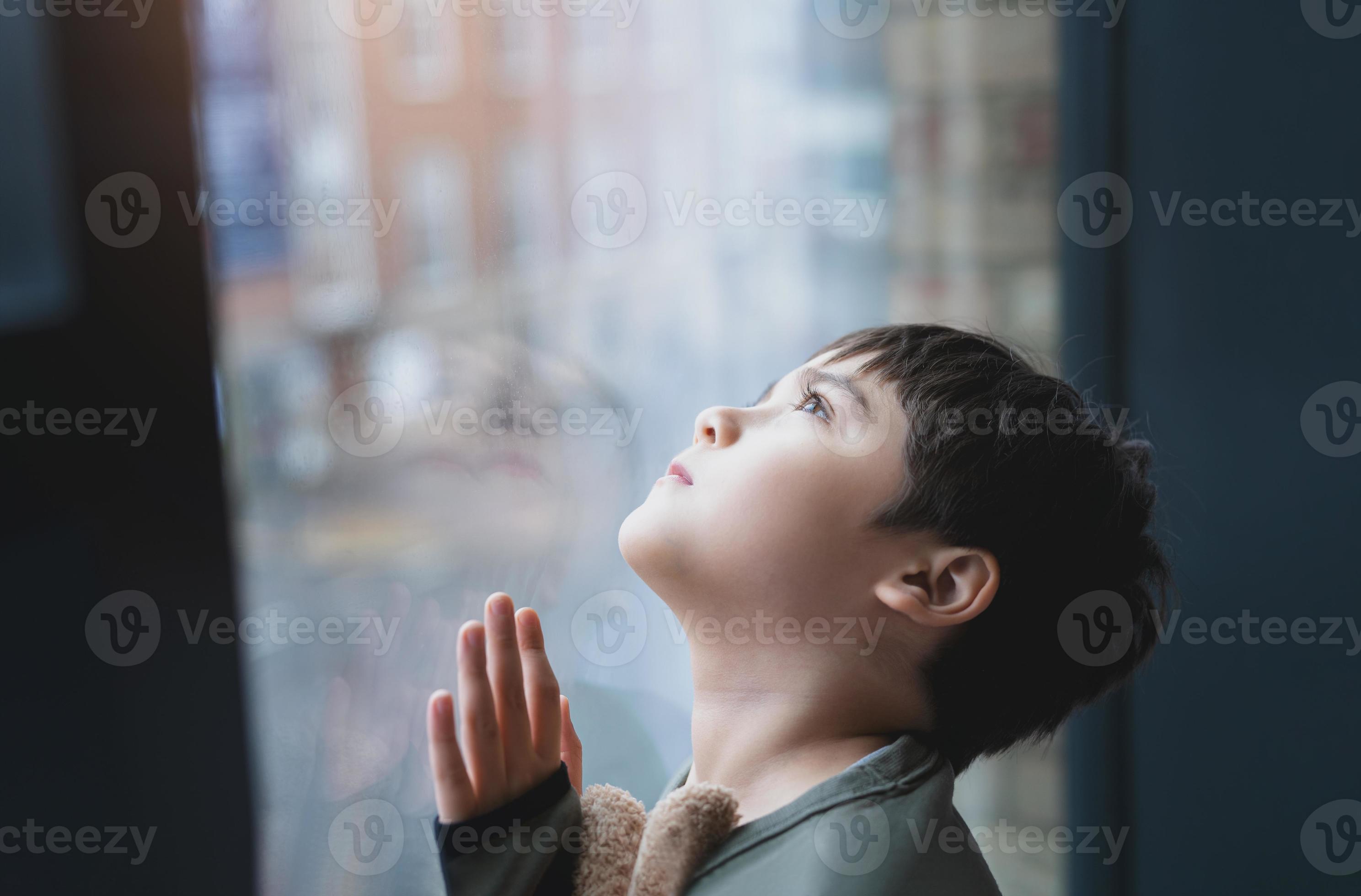 Young kid standing next to window looking up to sky with curious face ... Young kid standing next to window looking up to sky with curious face ...