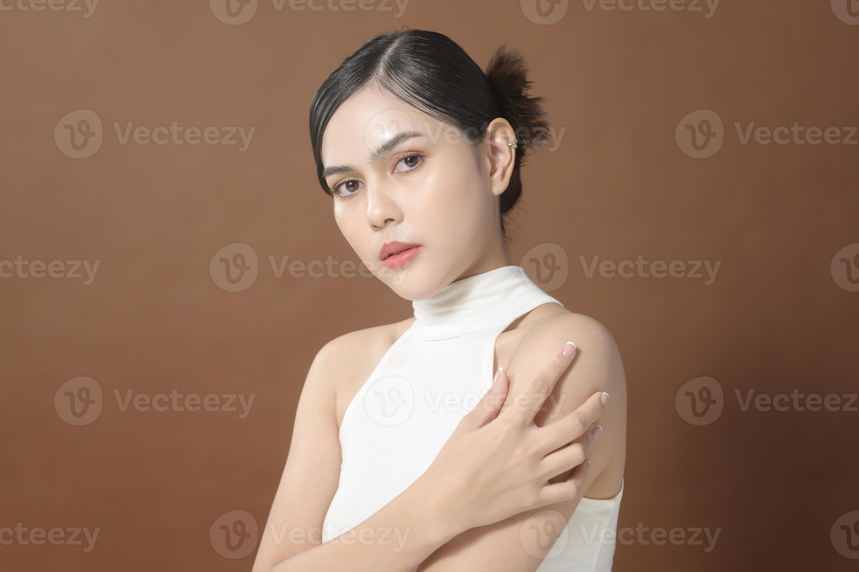 A young woman with beautiful face smiling, touching her skin over brown background , beauty skin ...