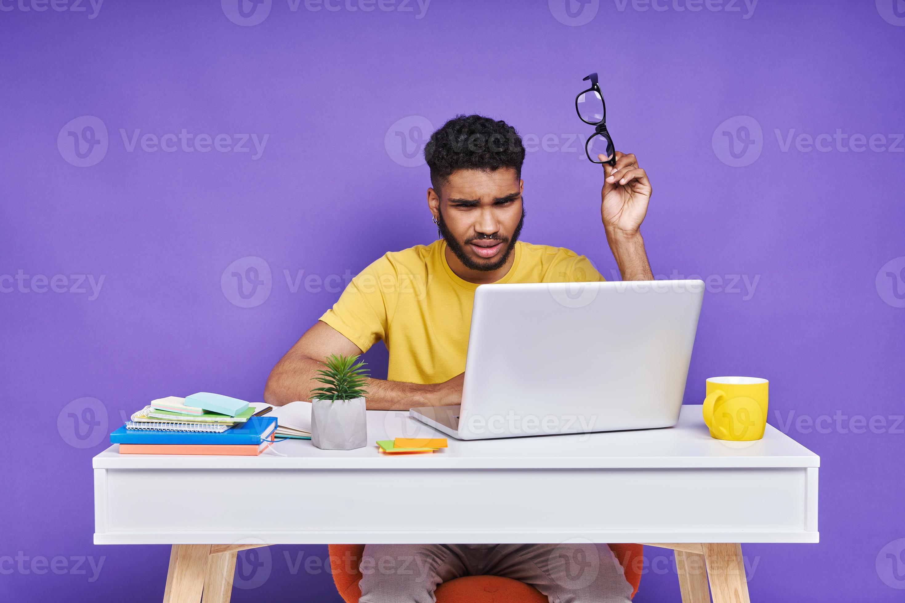Frustrated man looking at laptop while sitting at the desk against ...
