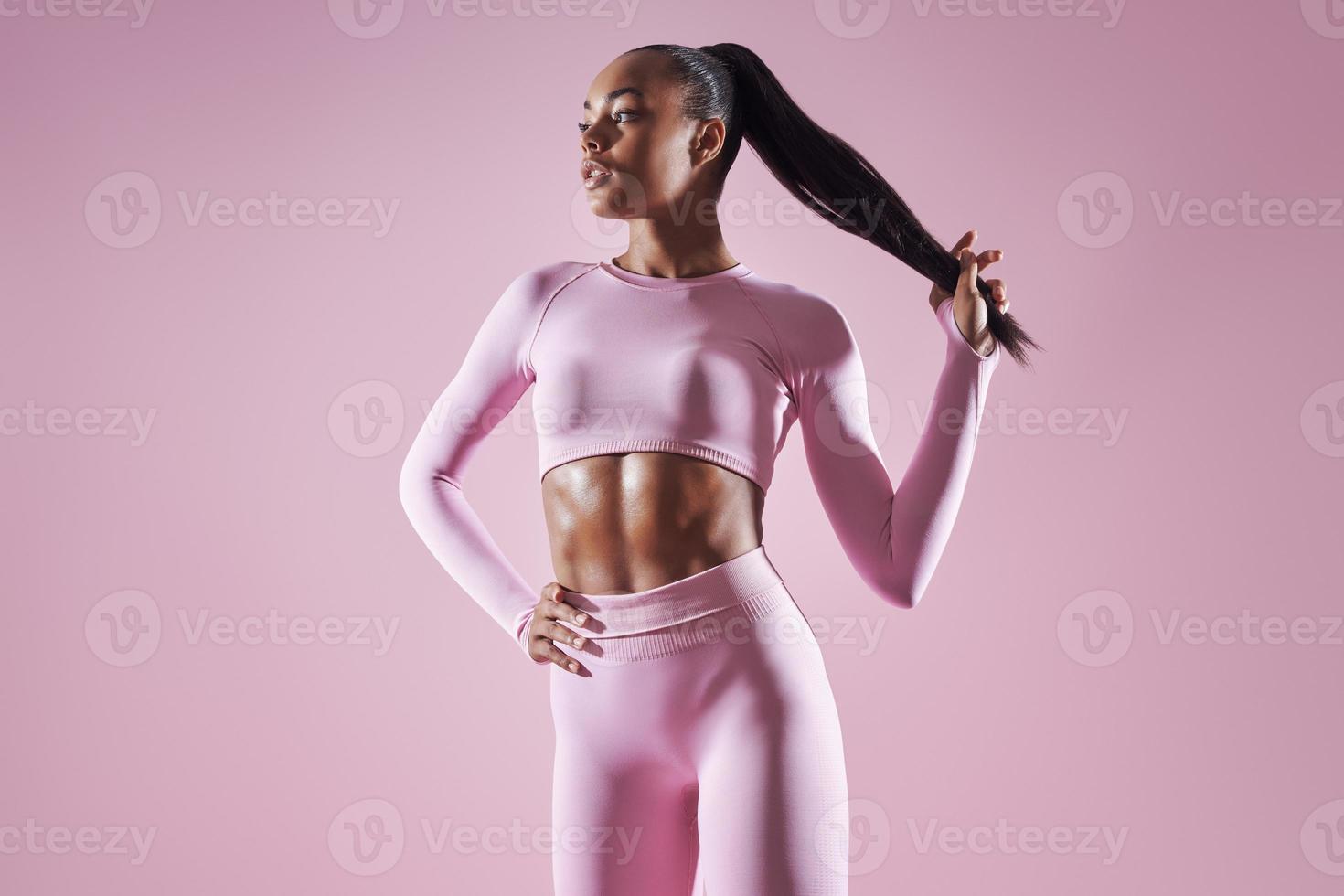Confident African Woman In Sports Clothing Adjusting Her Hair Against Pink Background 10153946