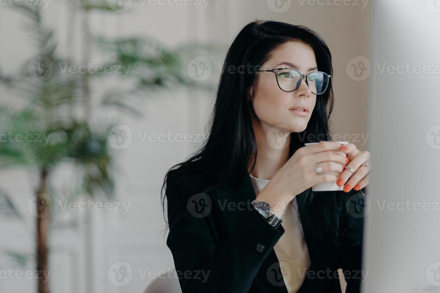 foto de una redactora morena concentrada que bebe café, trabaja en tareas creativas, usa ...