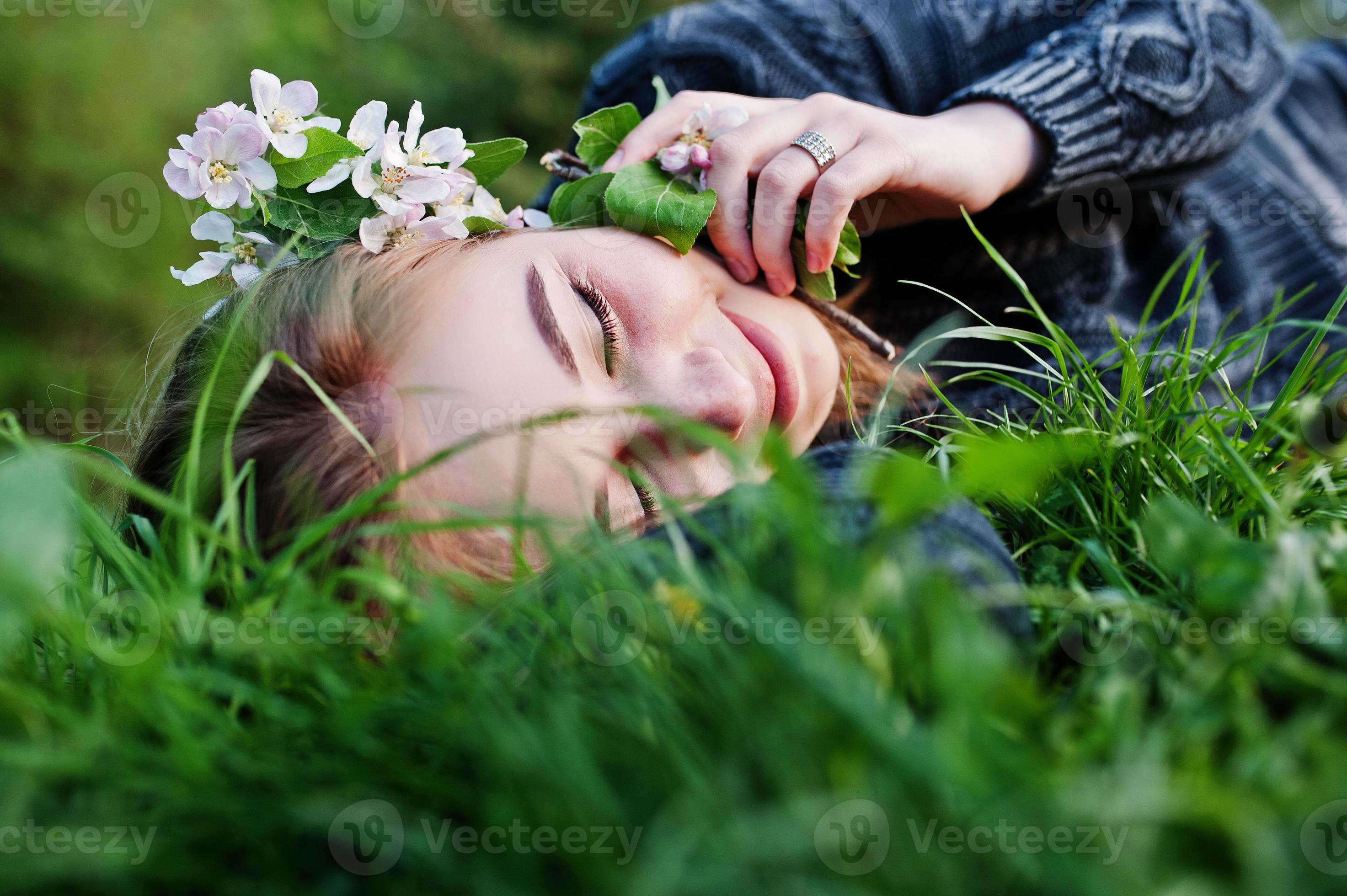 Young Brunette Girl Lying On Green Grass With Branches Of Blossom Tree
