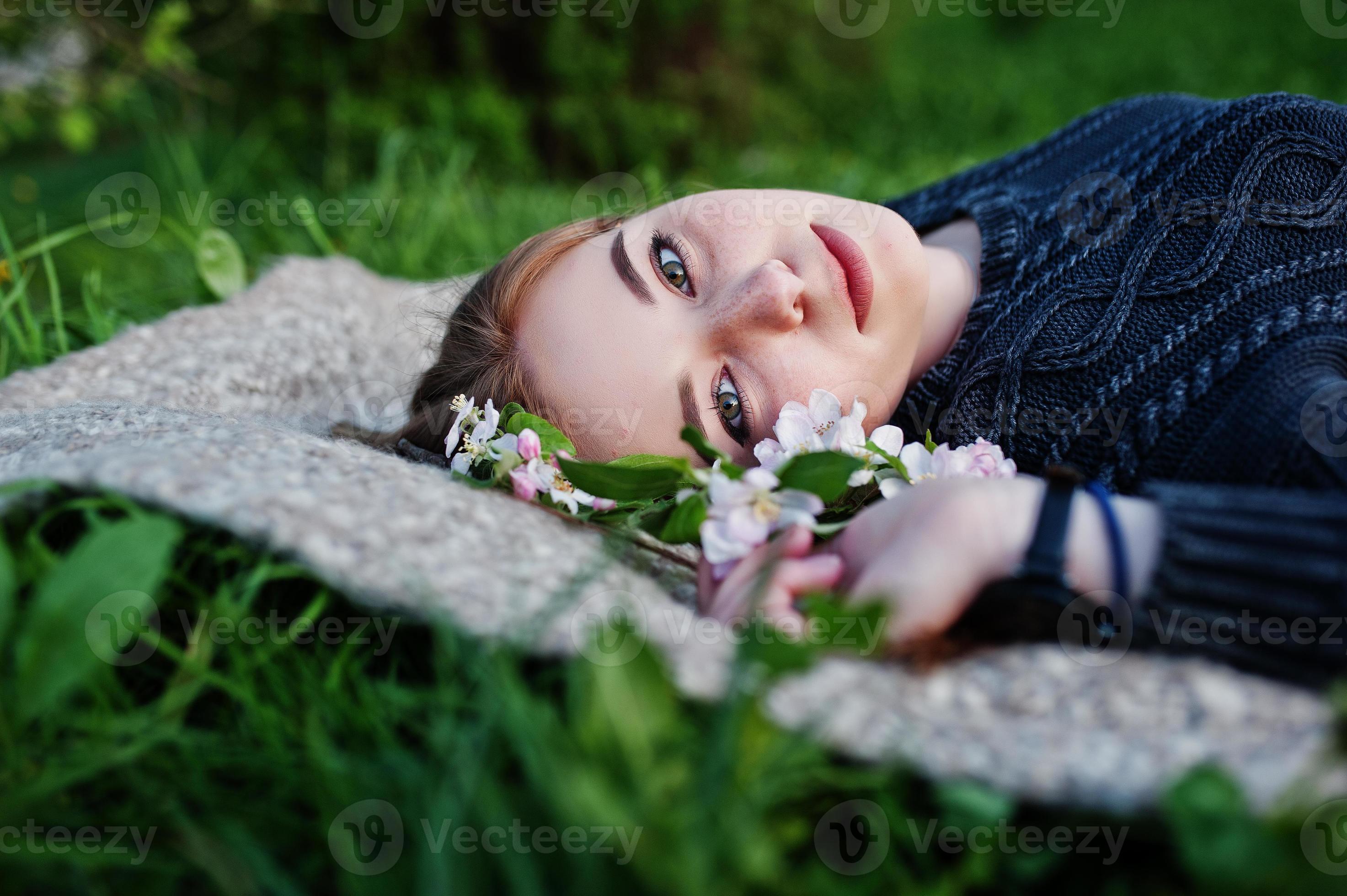 Young Brunette Girl Lying On Green Grass With Branches Of Blossom Tree