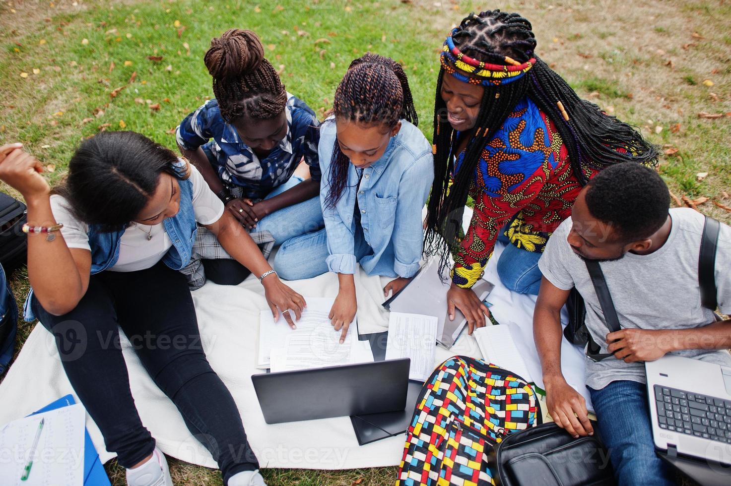 Group of five african college students spending time together on campus at university yard ...