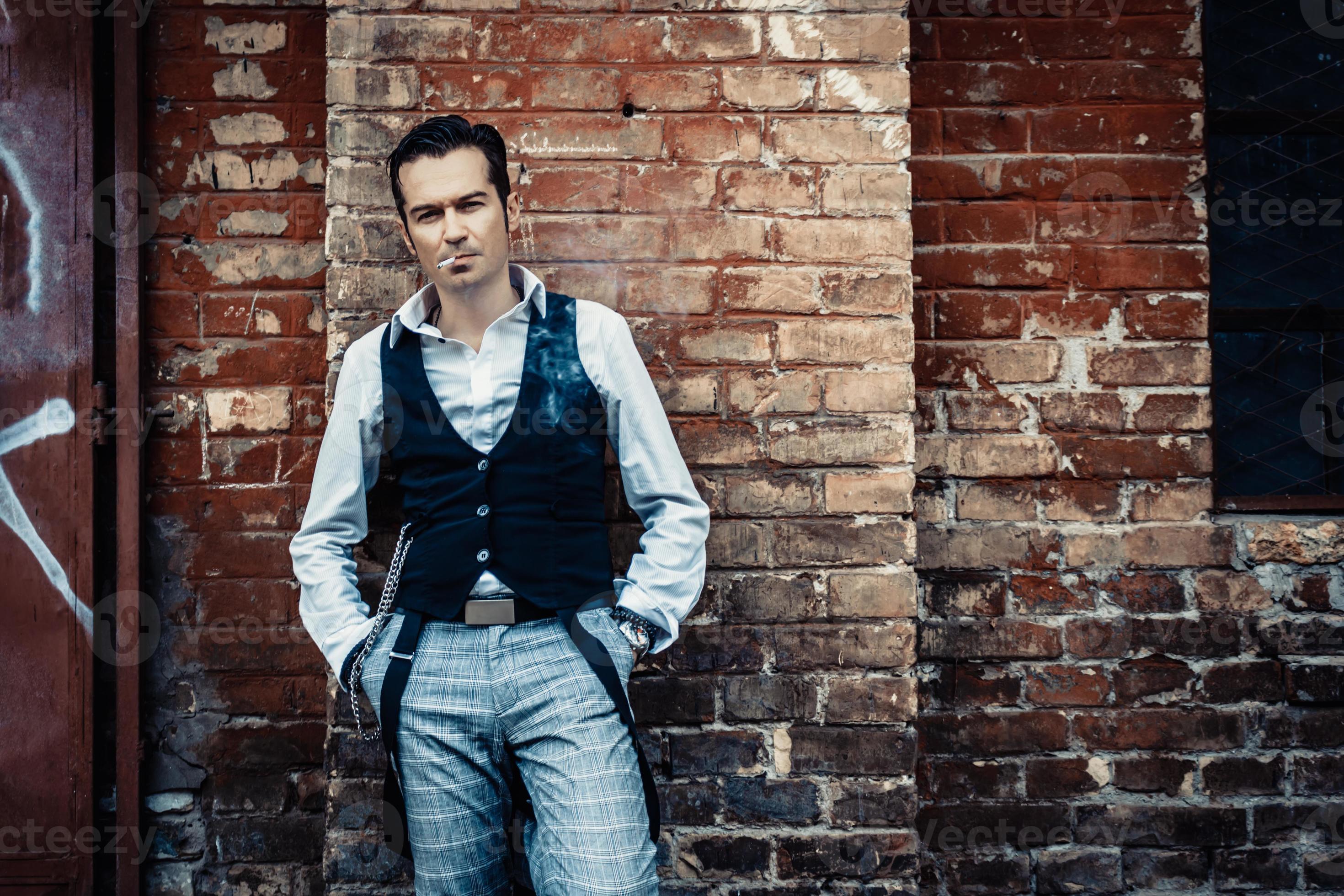 Confident retro-styled man smoking cigarette while leaning on a wall ...