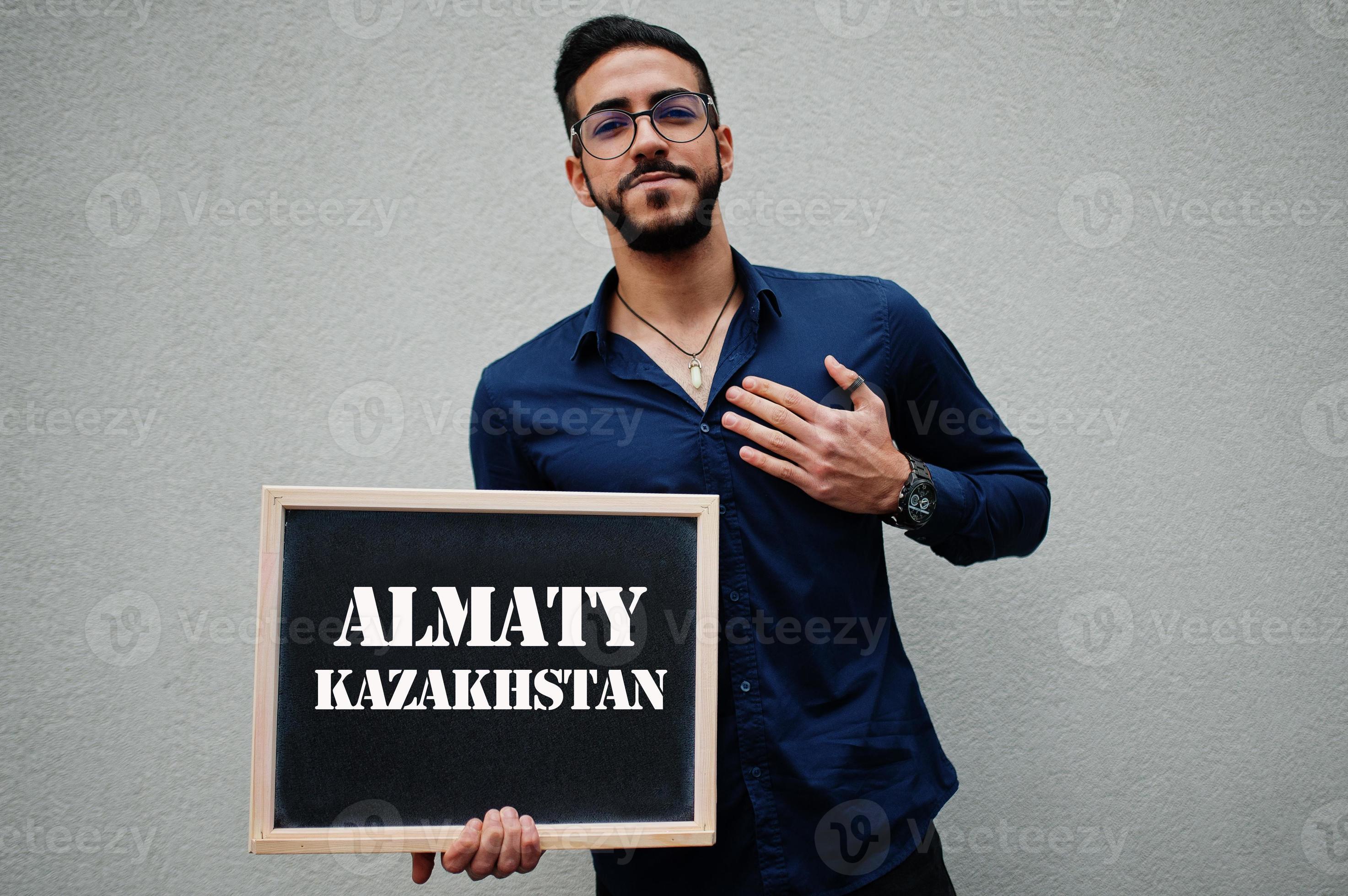 Arab man wear blue shirt and eyeglasses hold board with Almaty Kazakhstan inscription. Largest ...