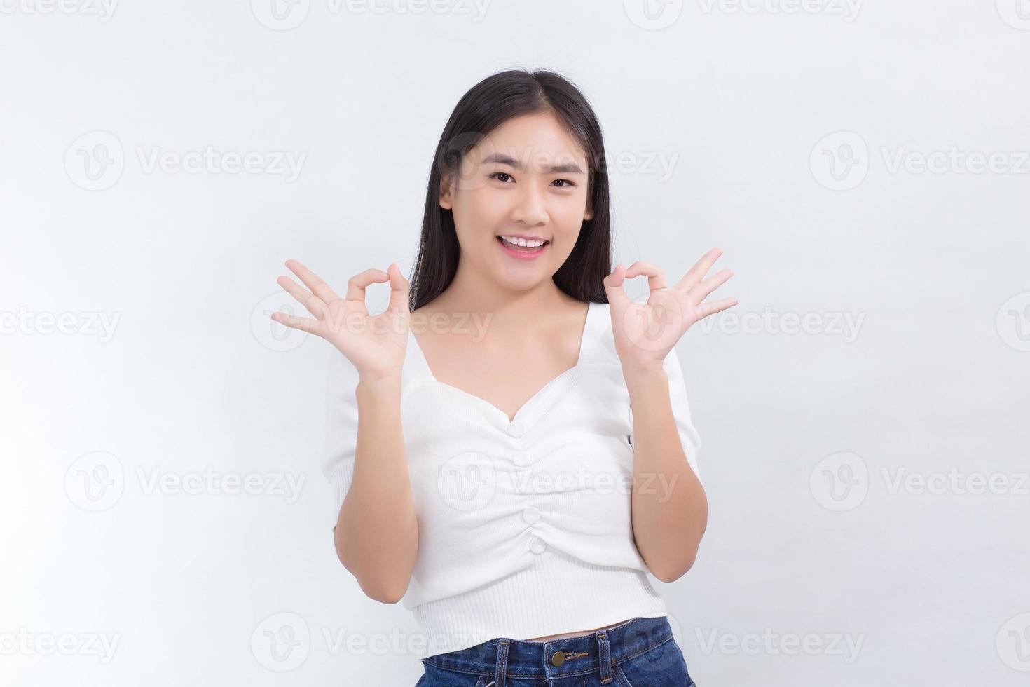 Asian woman with long black hair wears white shirt and shows hand okey sign on white background ...