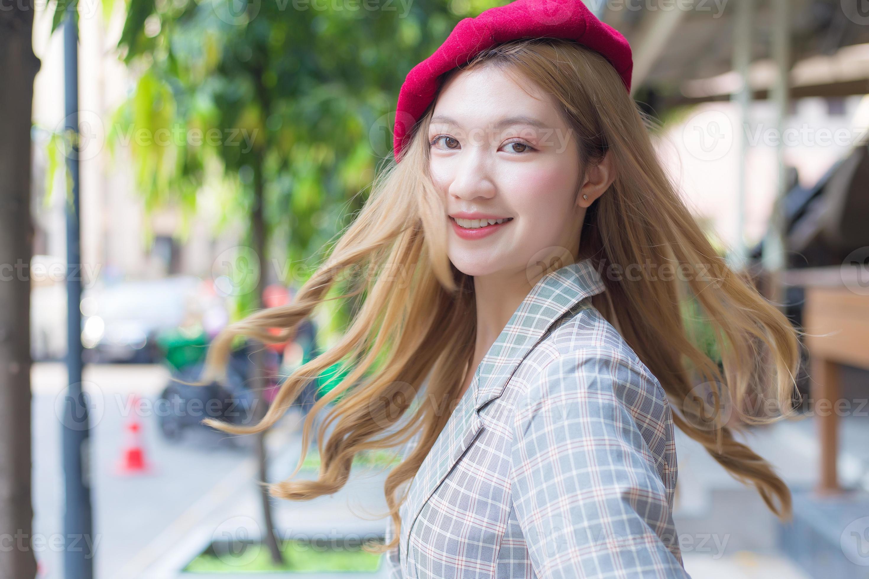 Asian beautifu lady with bronze hair wears red cap and turns to face on the street background ...