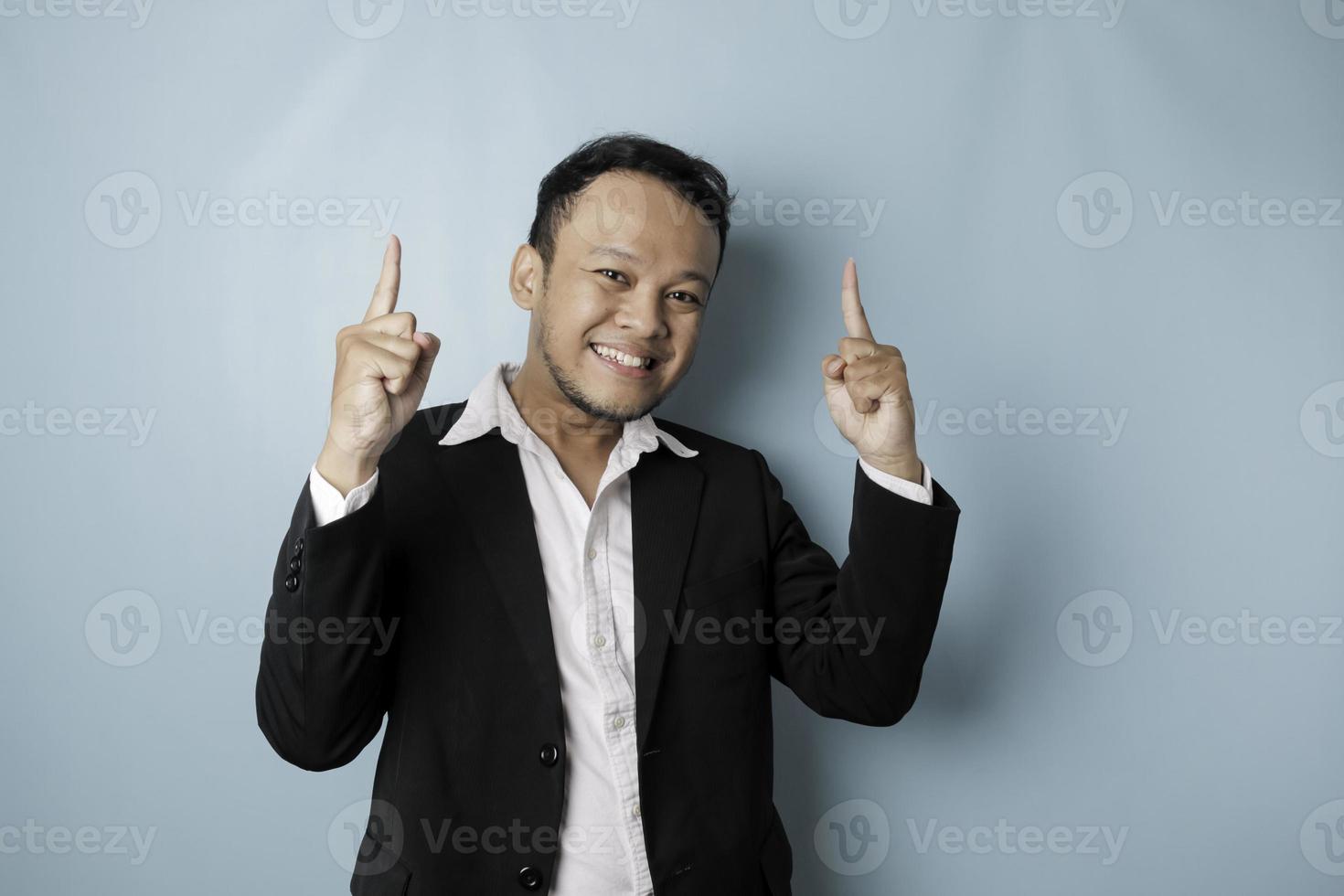 Excited Asian man wearing suit pointing at the copy space upside him ...
