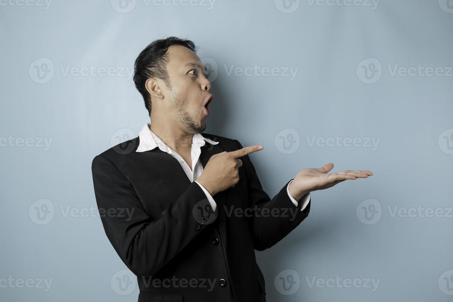 Shocked Asian man wearing suit pointing at the copy space beside him ...