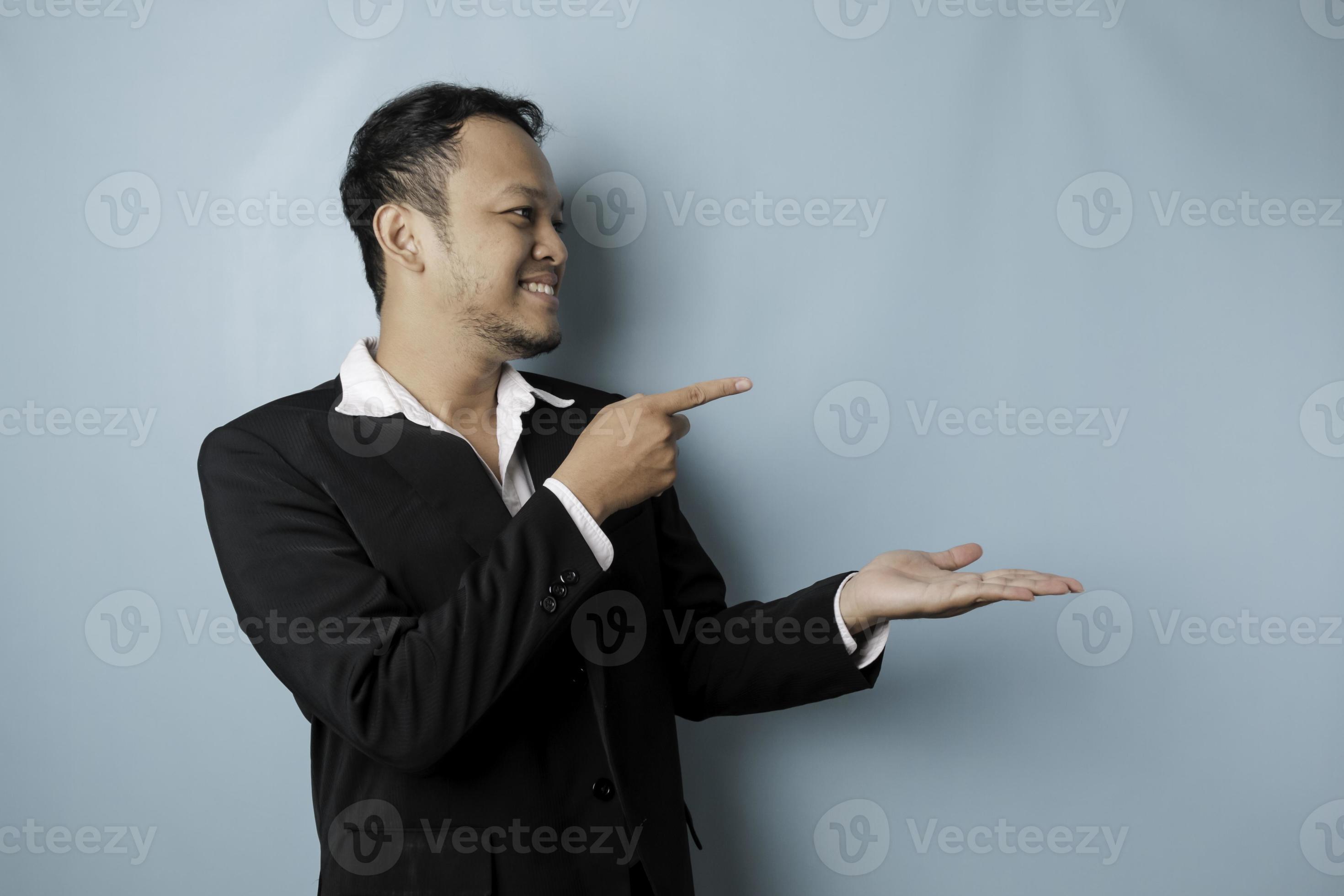 Excited Asian man wearing suit pointing at the copy space beside him ...