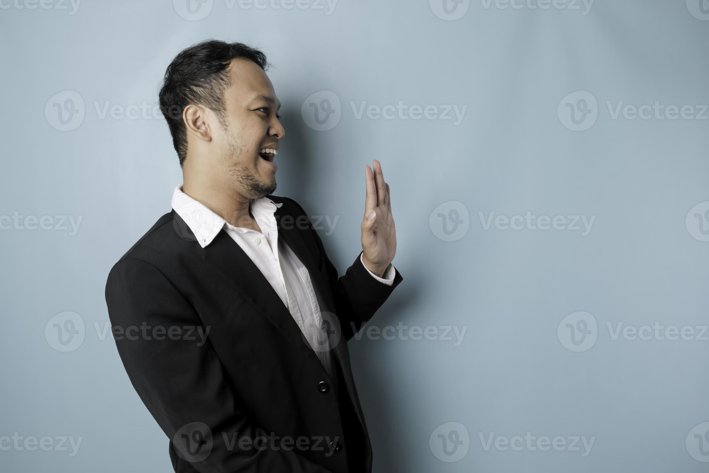 Excited Asian man wearing suit pointing at the copy space beside him ...