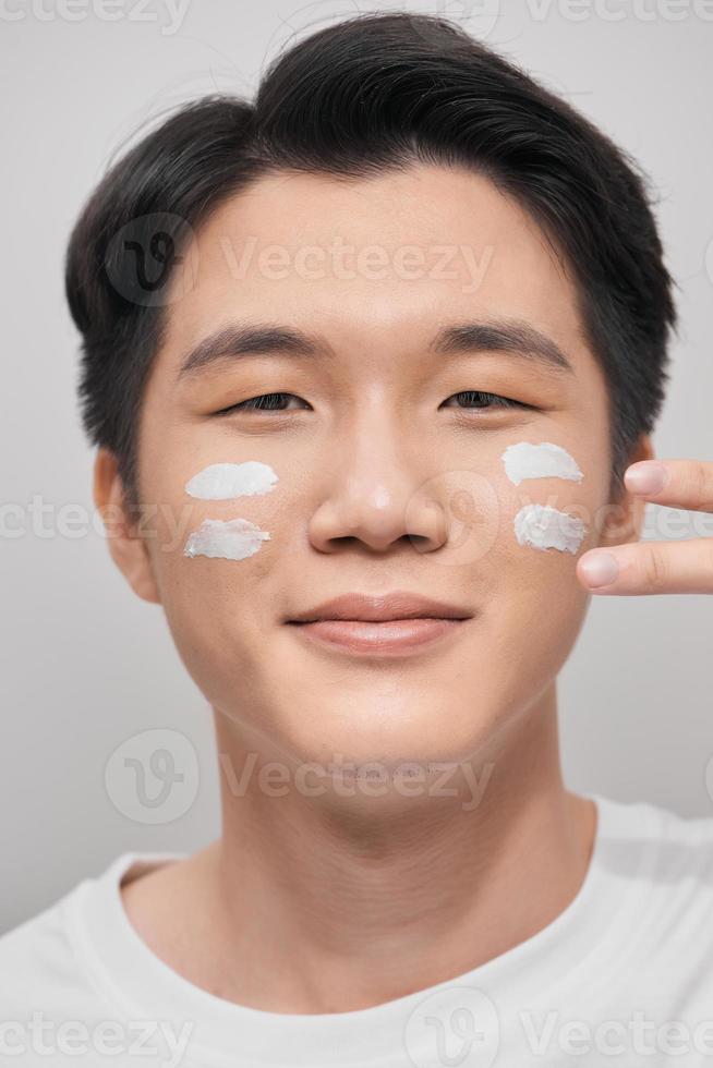 Skin care. Portrait of handsome young man applying cream to his face ...