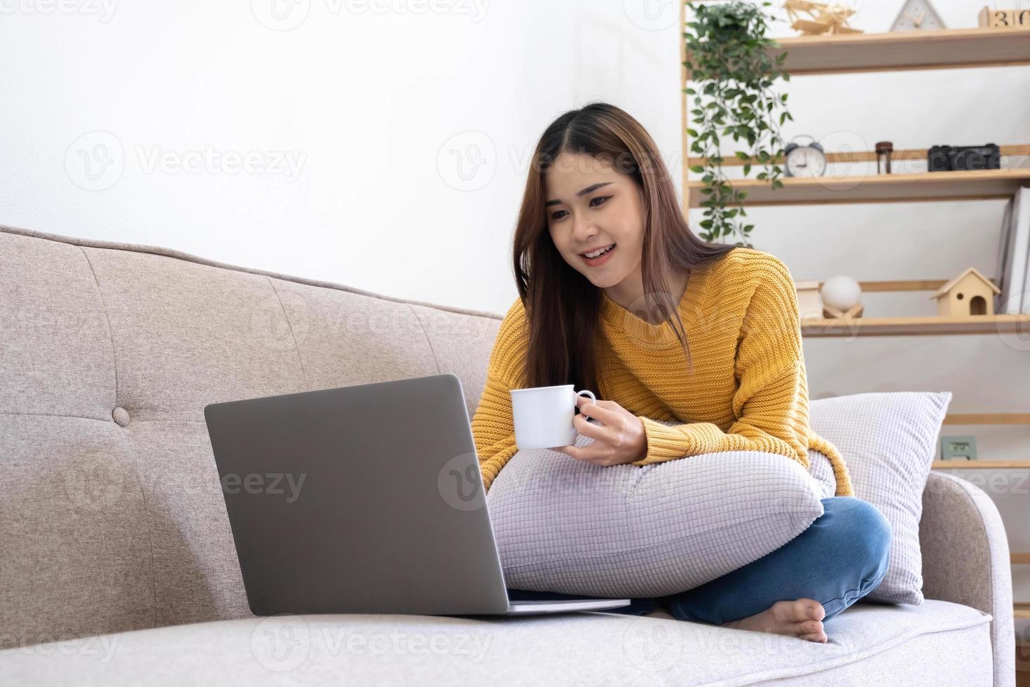 Young asian business woman work from home with laptop computer and drinking coffee on sofa in ...