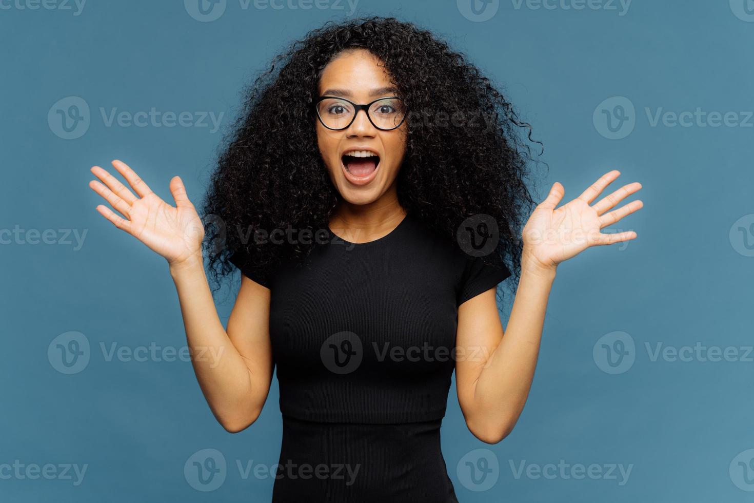 Emotional Excited Dark Skinned Lady Raises Palms Keeps Mouth Wide