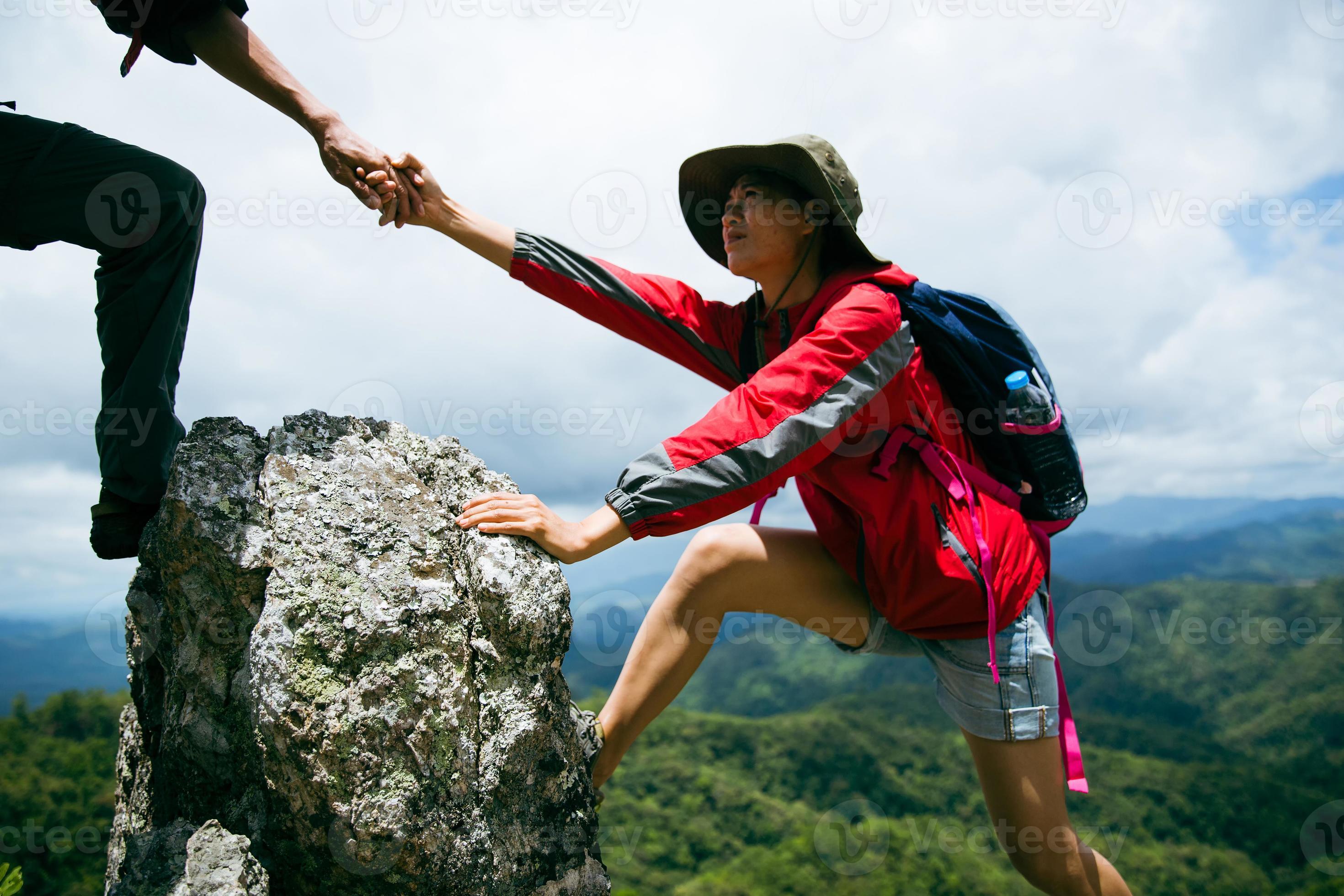 Person hike friends helping each other up a mountain. Man and woman giving a helping hand and ...