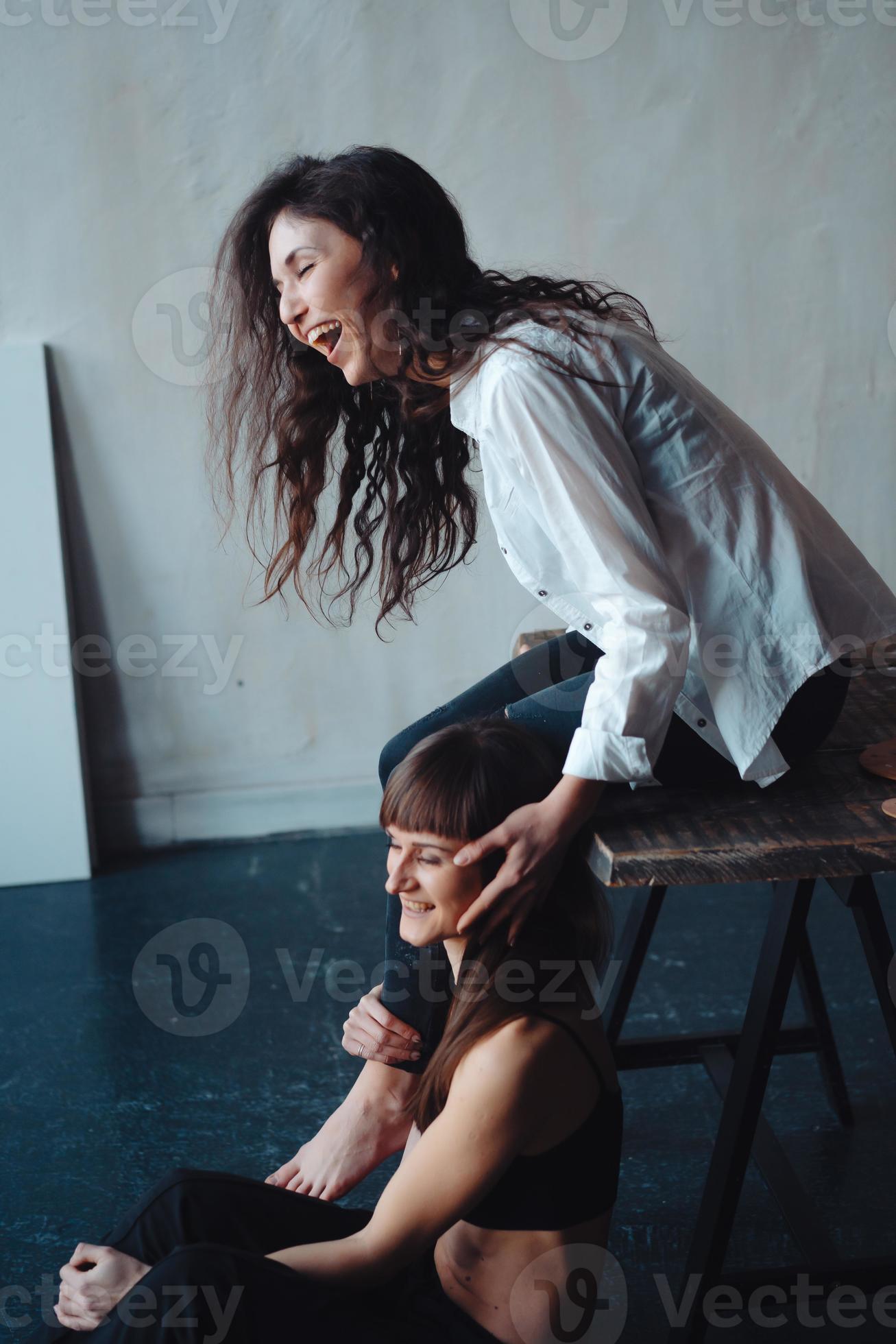 two girls are posing for the camera, one sitting on a chair, other on ...
