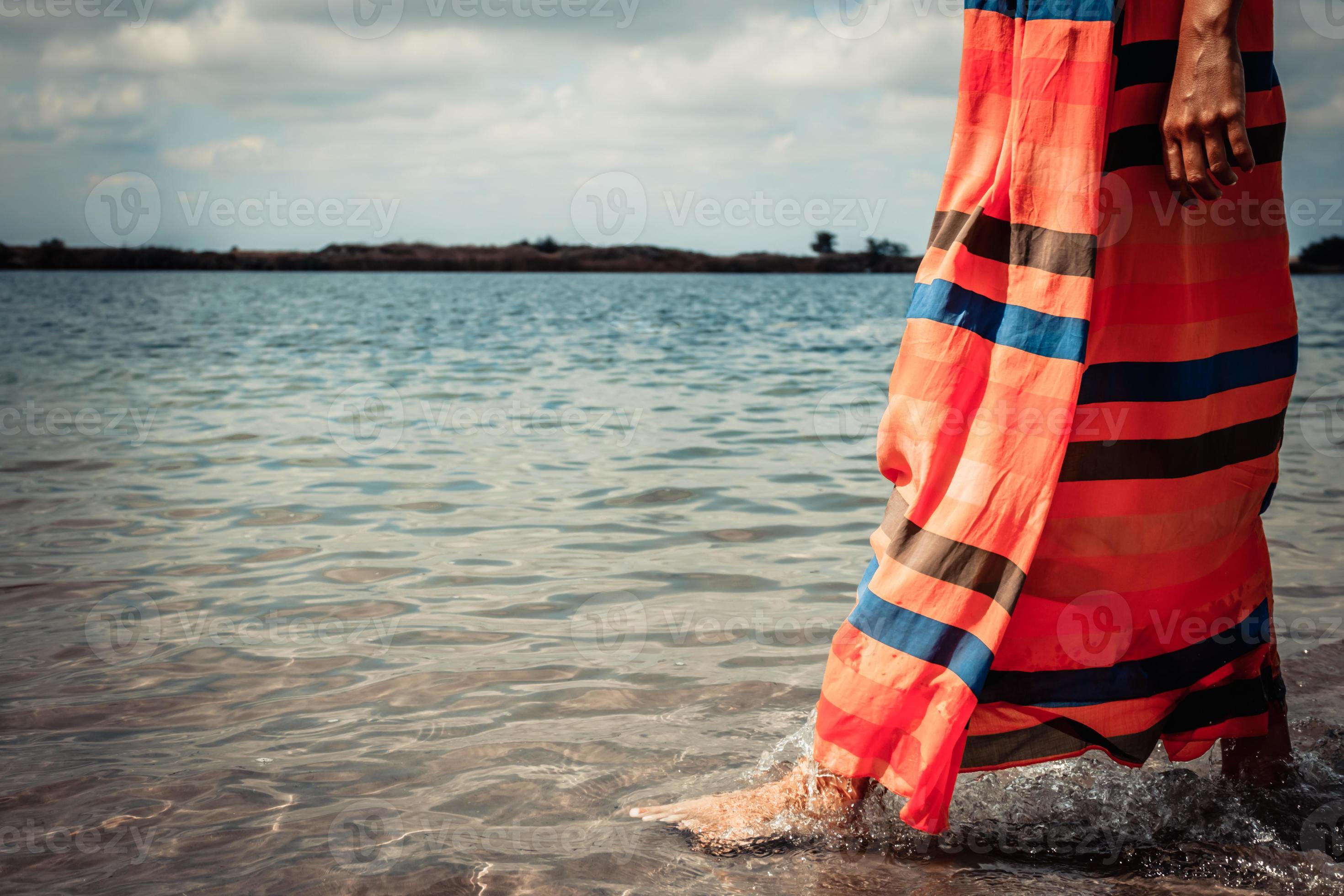 Unrecognizable woman walking through shallow water at the beach ...