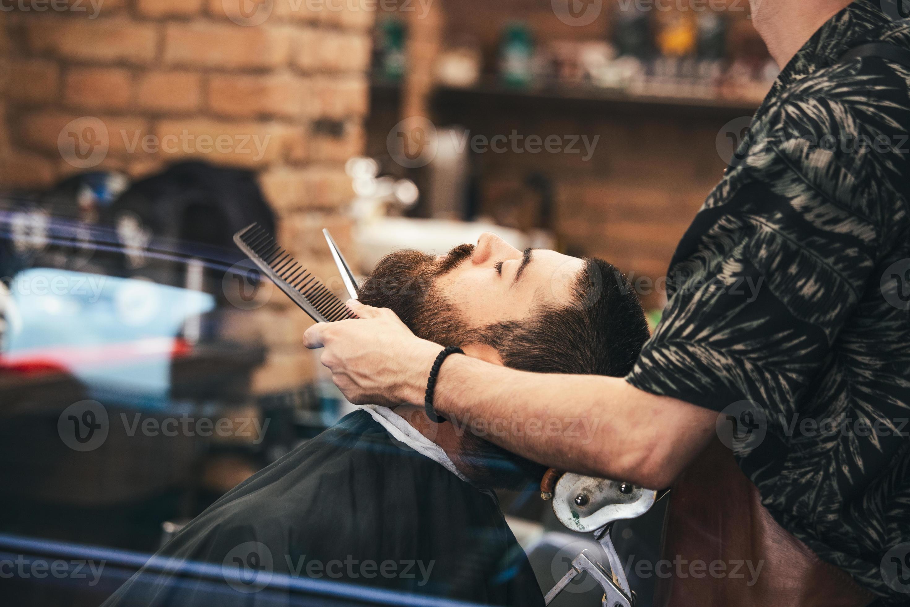 Bearded male sitting in an armchair in a barber shop while hairdresser ...