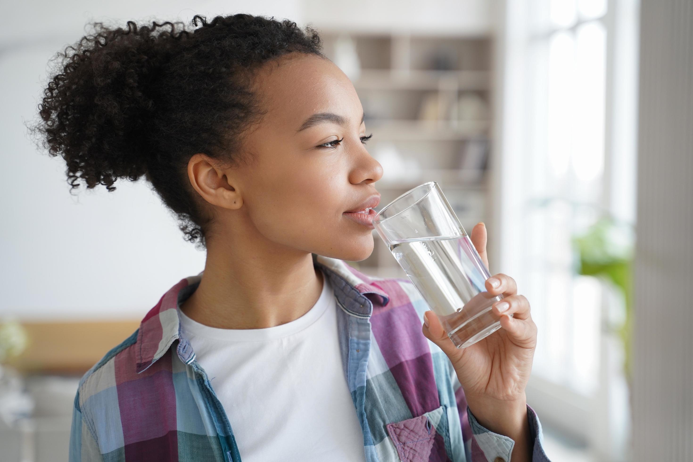 Mixed race young girl drink pure water from glass at home. Healthy lifestyle, morning routine ...