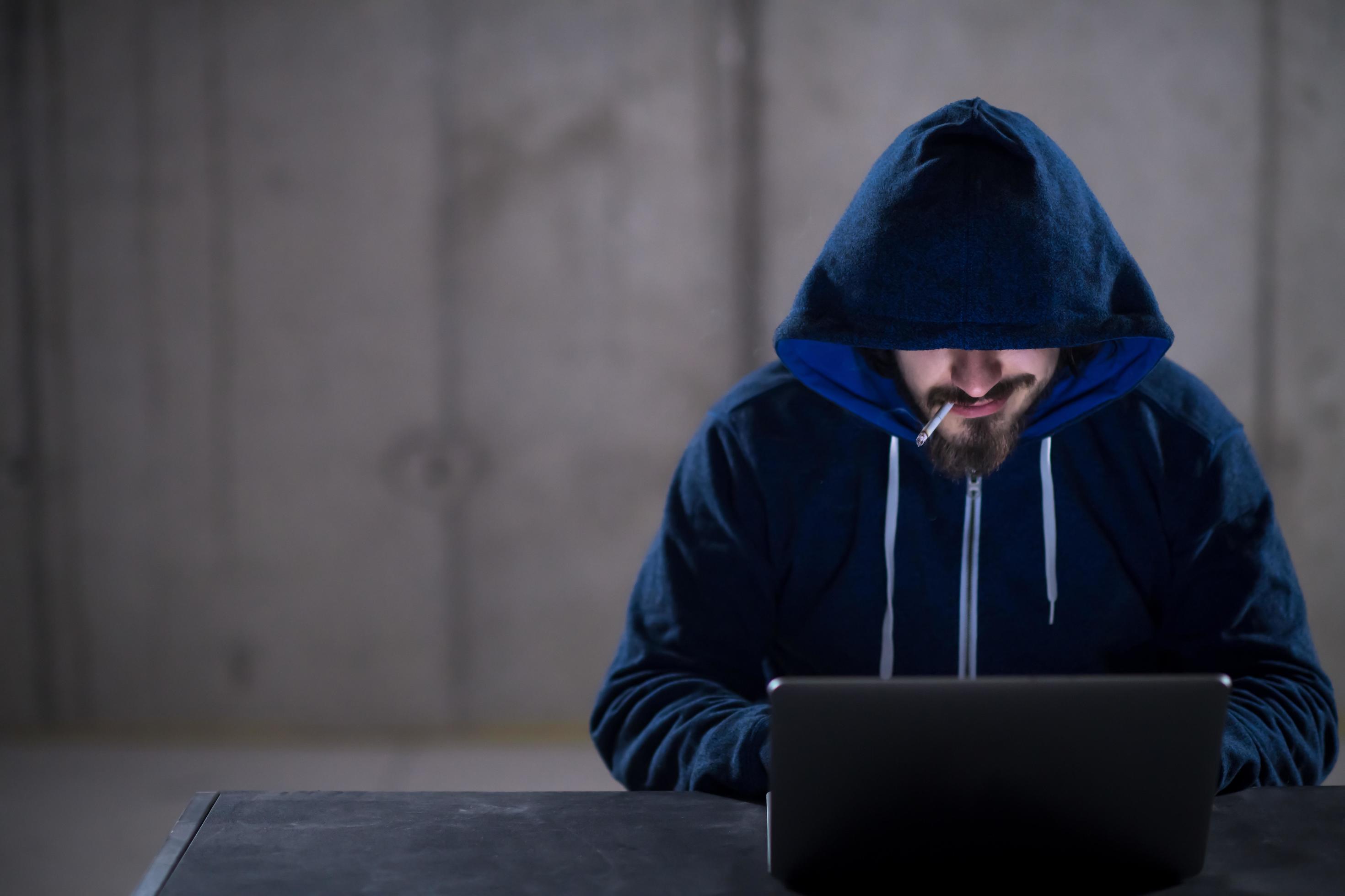 young hacker using laptop computer while working in dark office ...