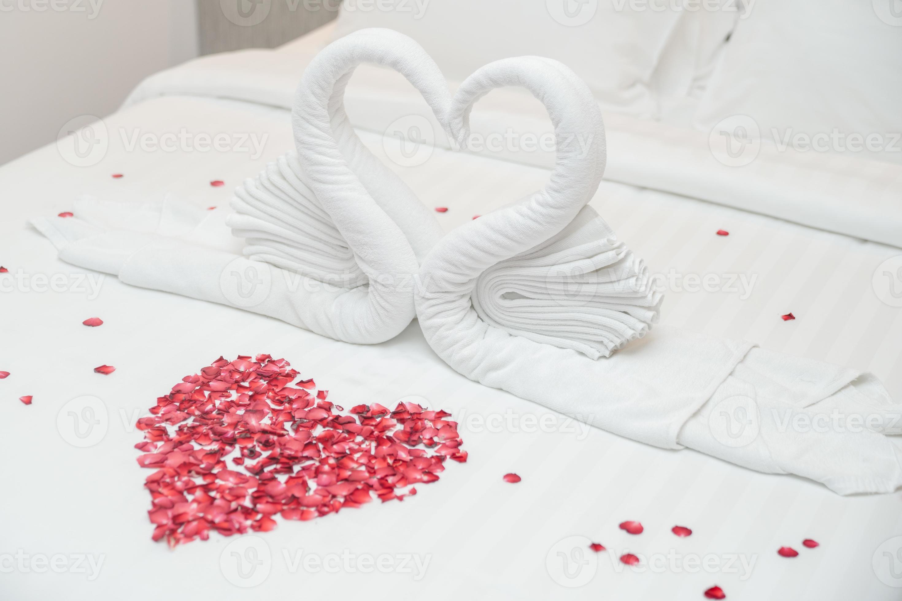 Swan towel on bed and rose petals in heart shape for honeymoon or wedding anniversary, romantic ...